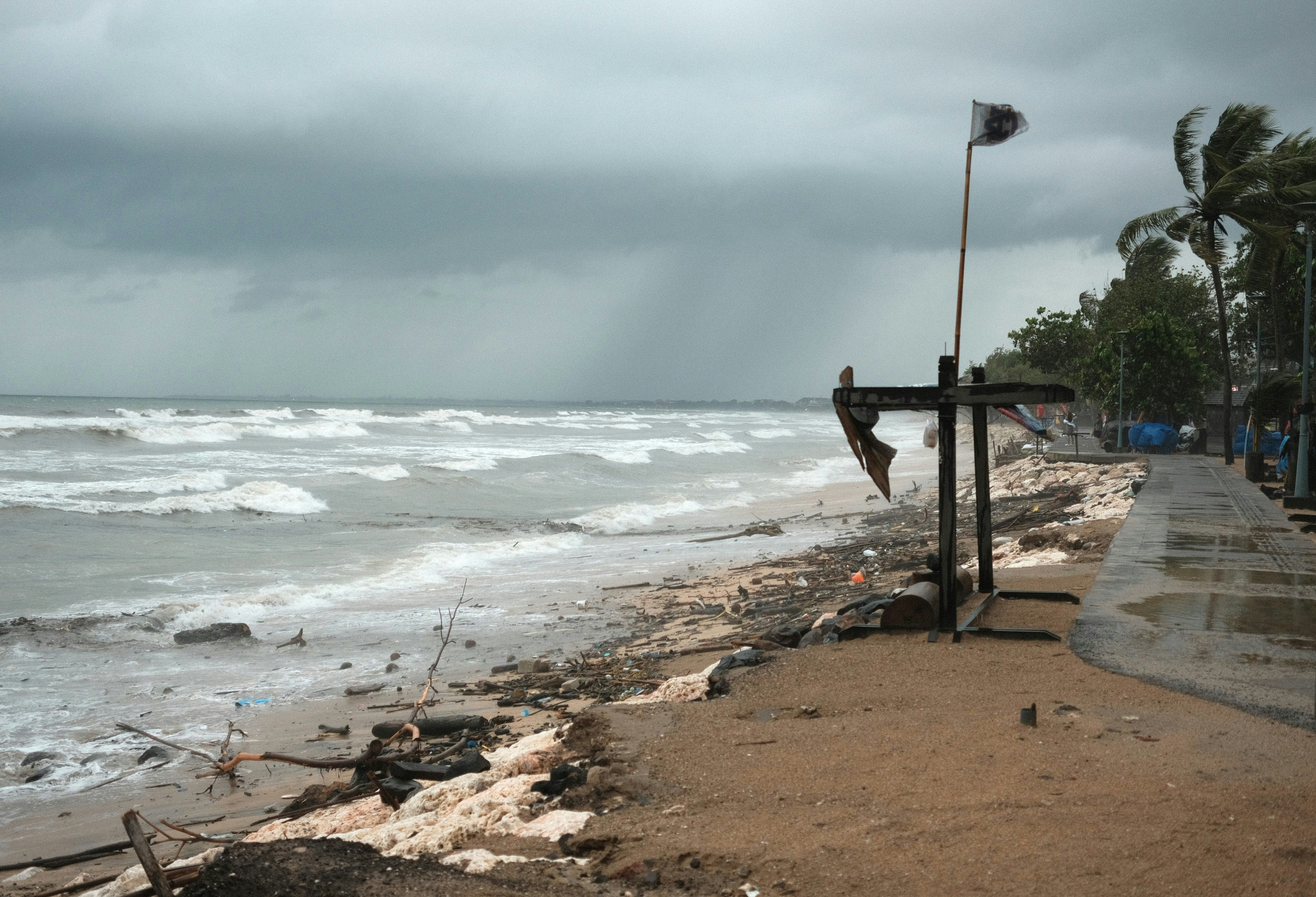 Overcast sky looms over a windswept beach with scattered debris along the shoreline.