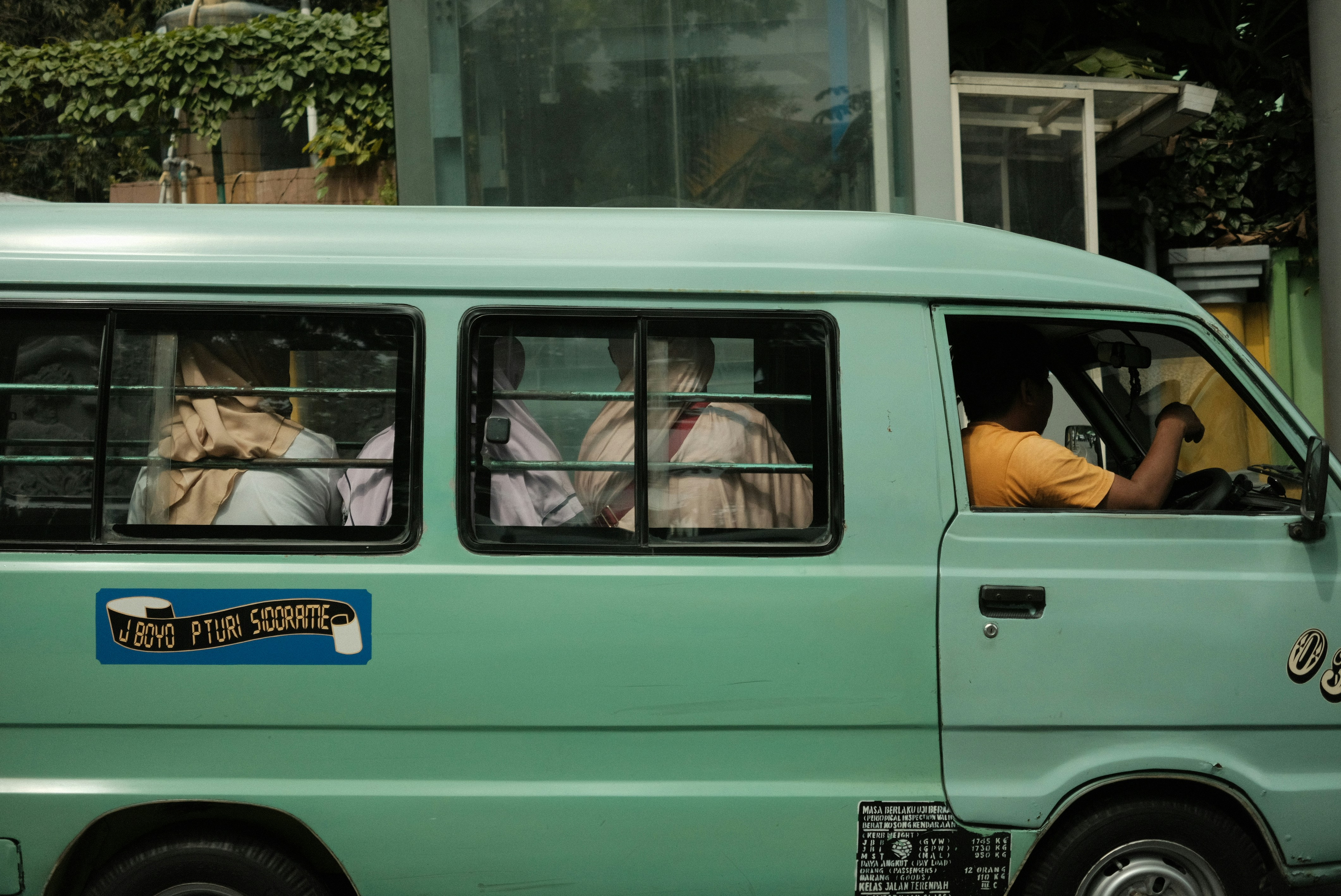 A green van driving down a street next to a tall building
