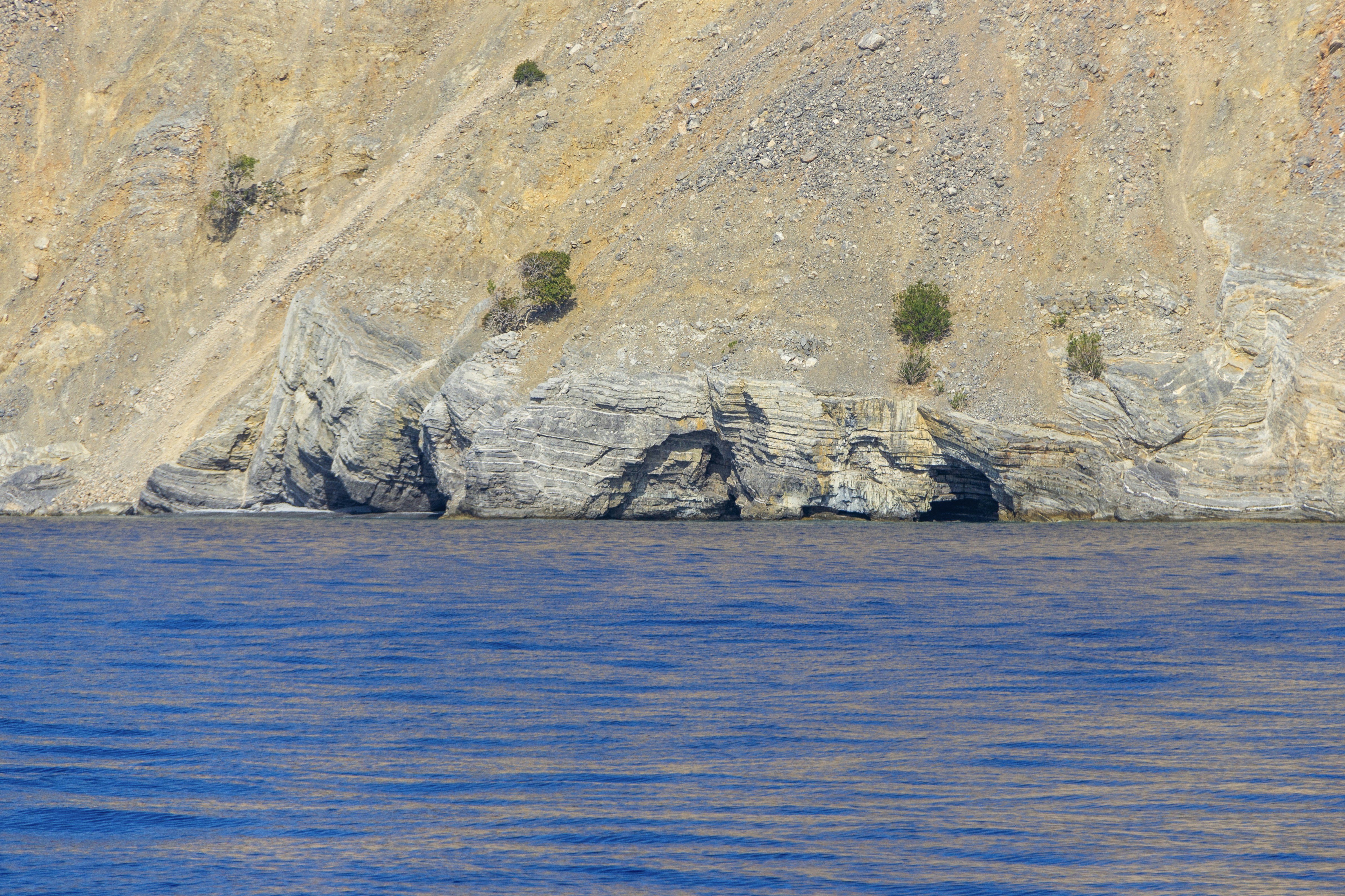 Rocky shore with rugged cliffs meeting a calm blue sea under clear skies.