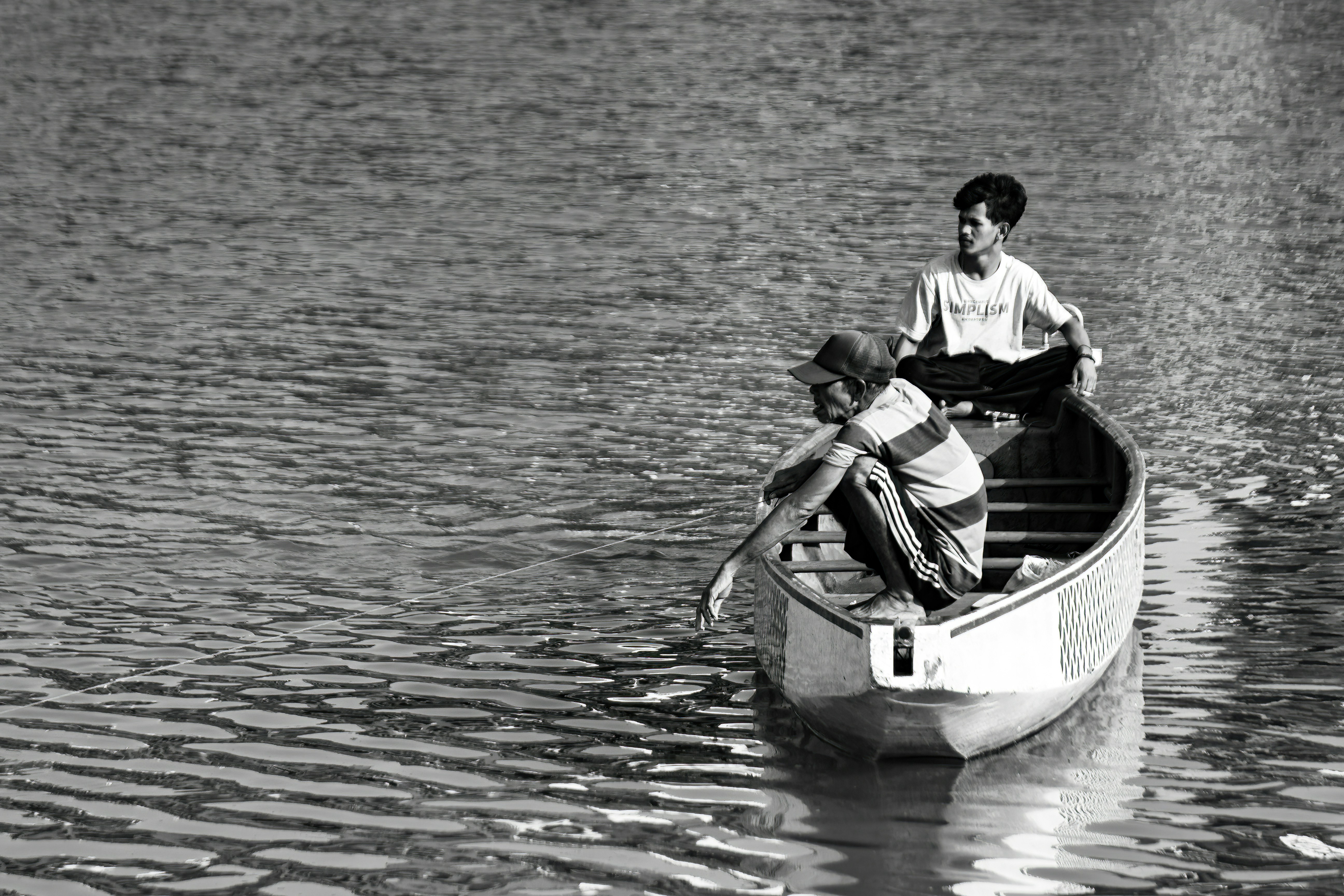 Two individuals in a canoe drift across a calm river, one leaning forward with an oar.
