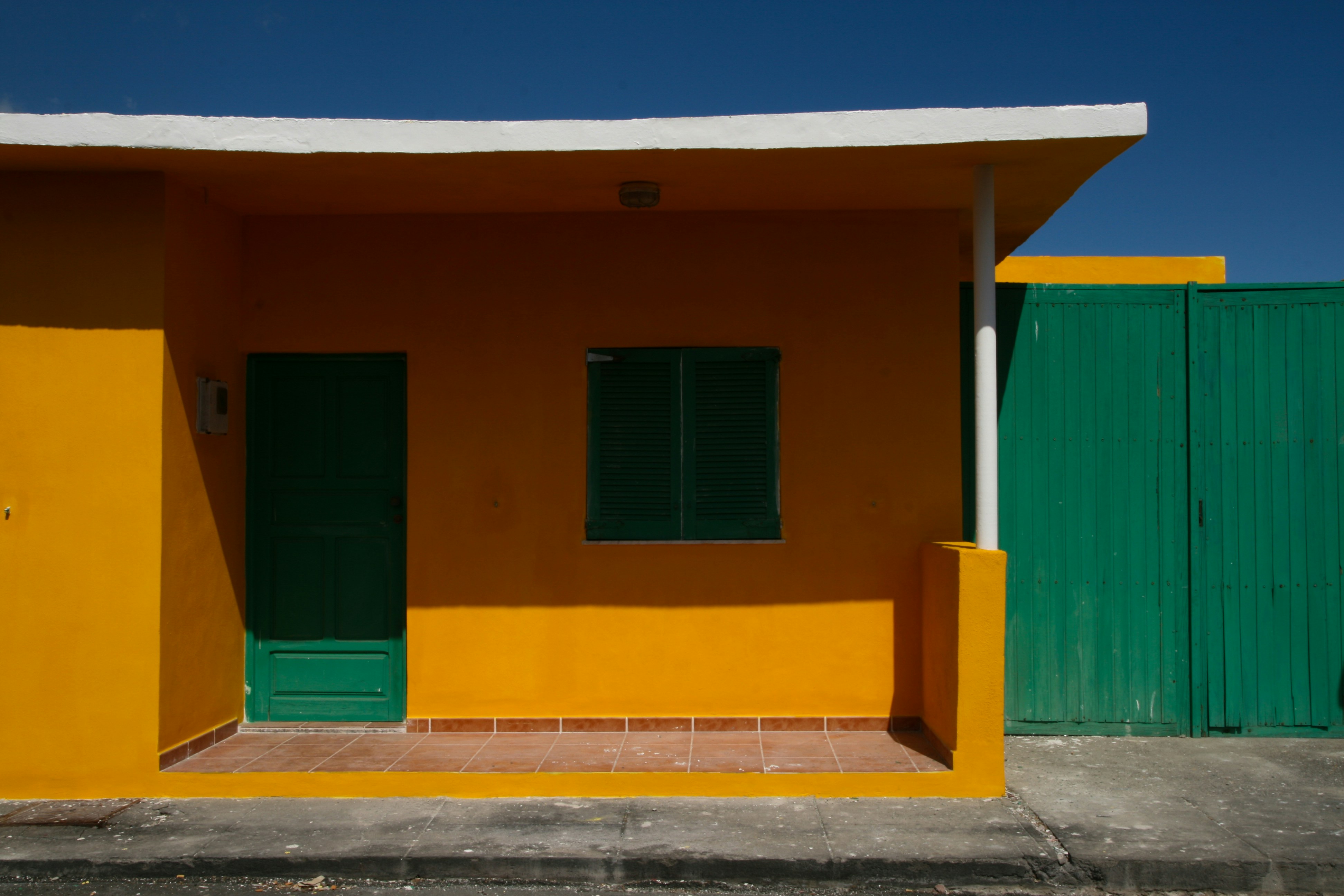 Bright yellow facade with green door and shutters under a clear blue sky.