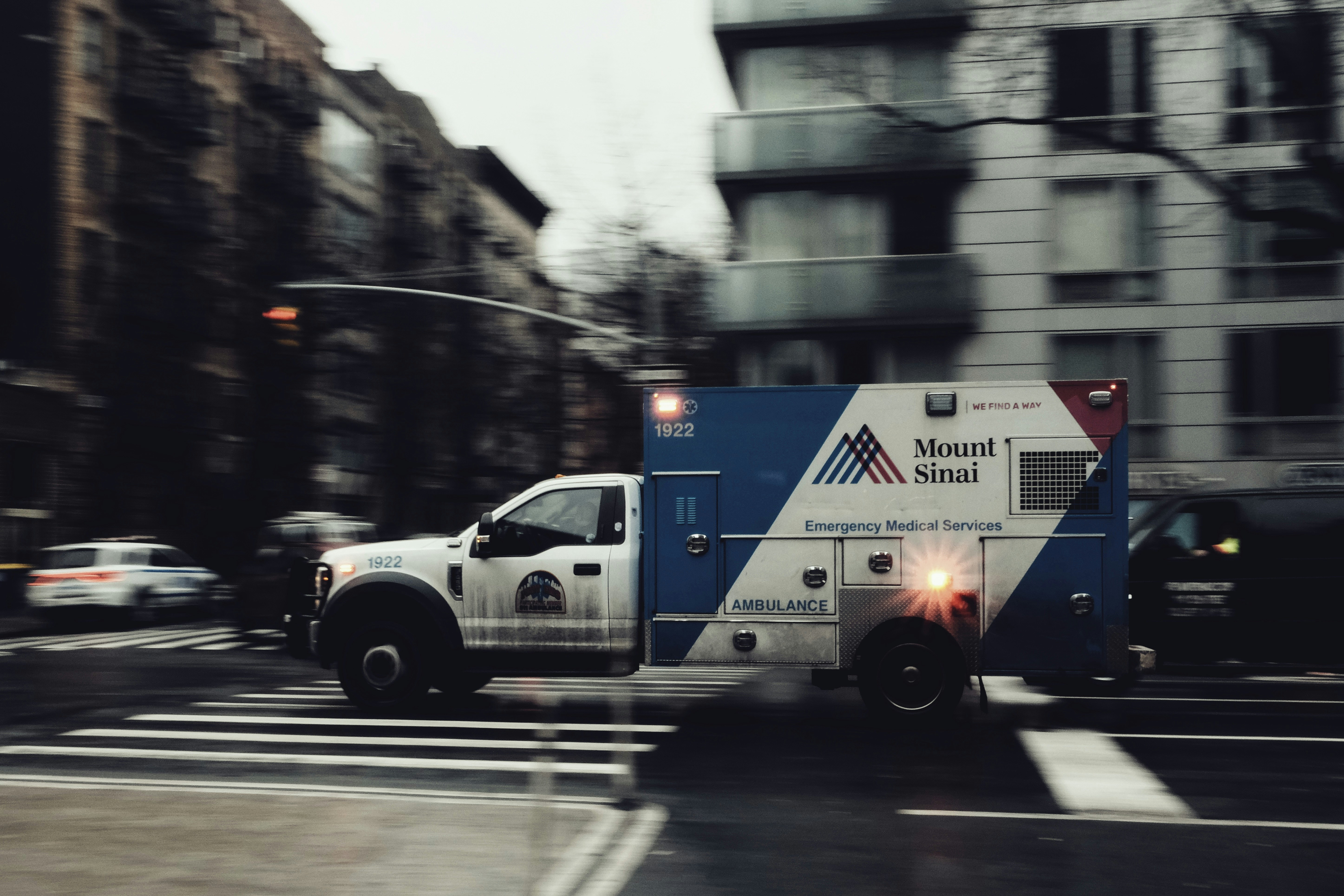 Ambulance speeding through a city intersection with blurred background of buildings.