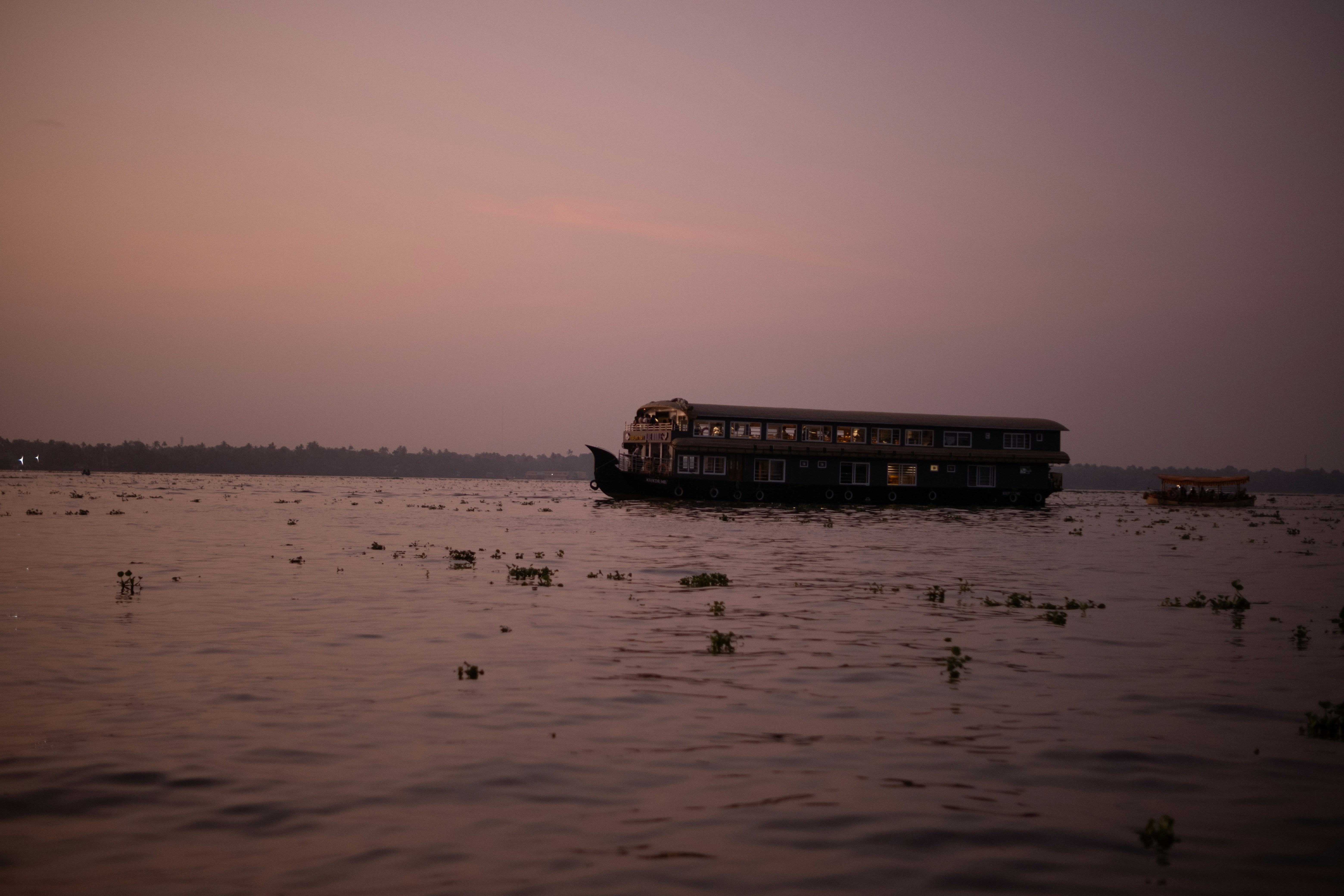 Traditional wooden houseboat gliding on a tranquil lake under a pink-hued sky.