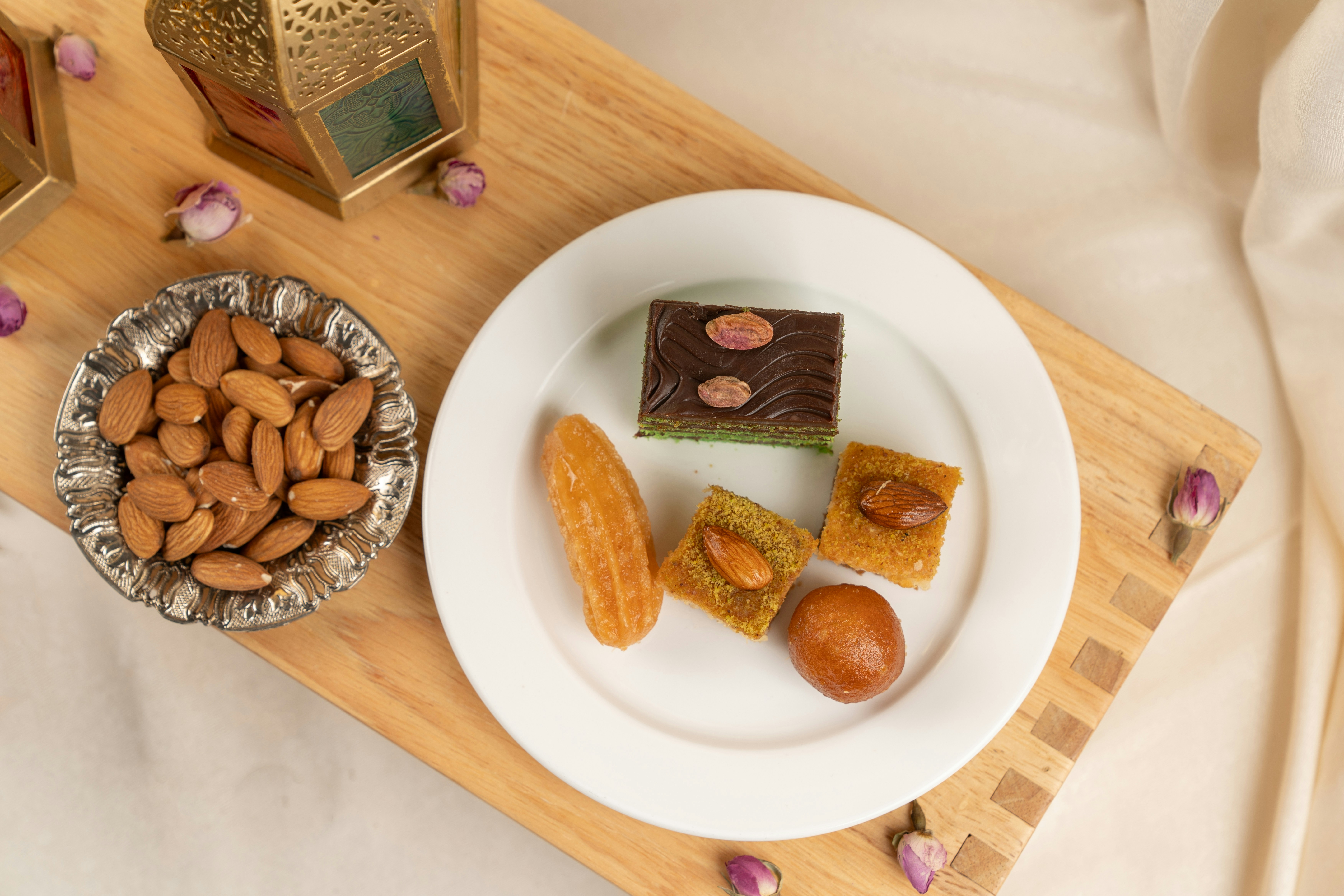 Assorted confections on a wooden board: chocolate square, pastry bites, and almonds
