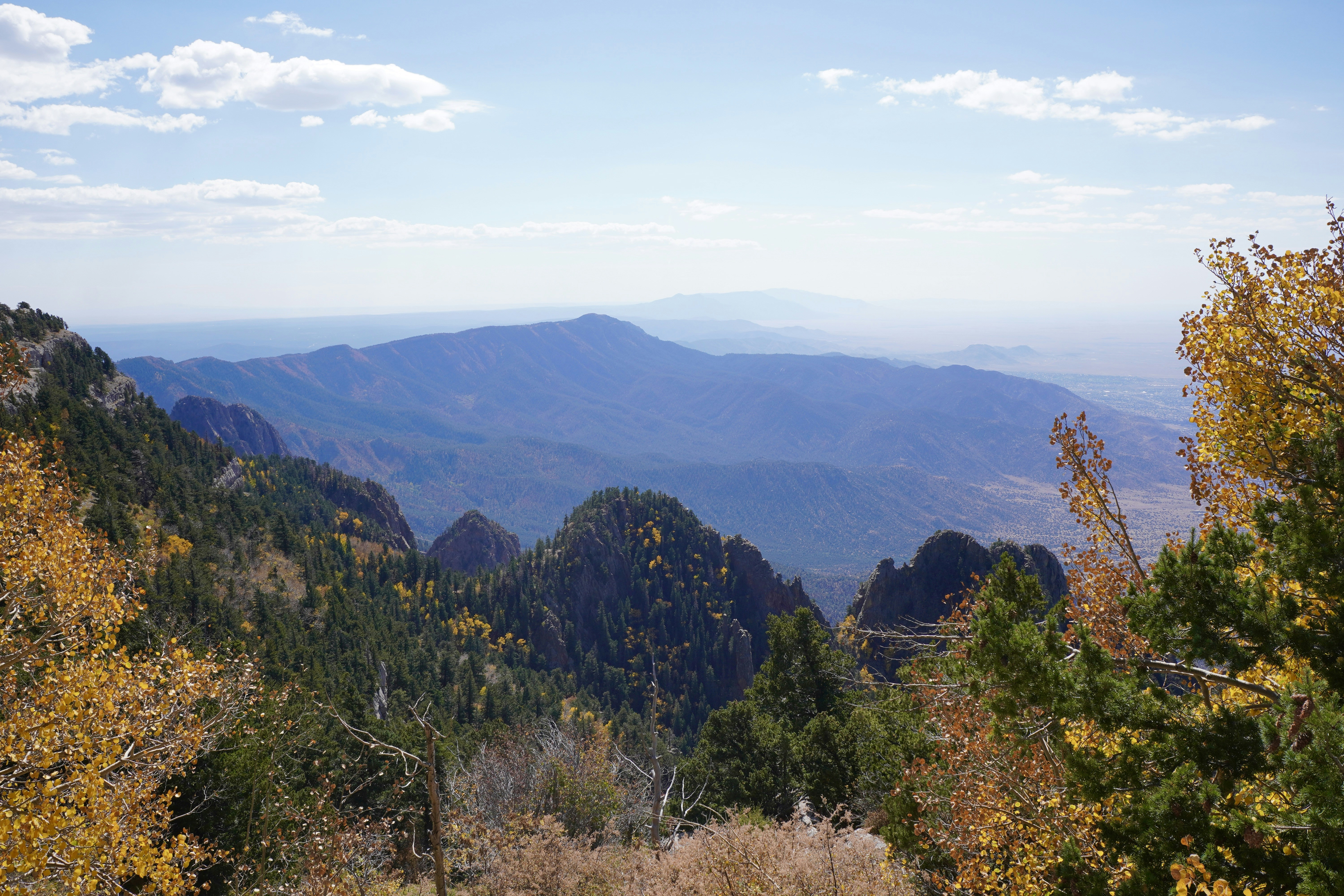 Golden autumn foliage frames rugged mountain ridges under a clear blue sky.