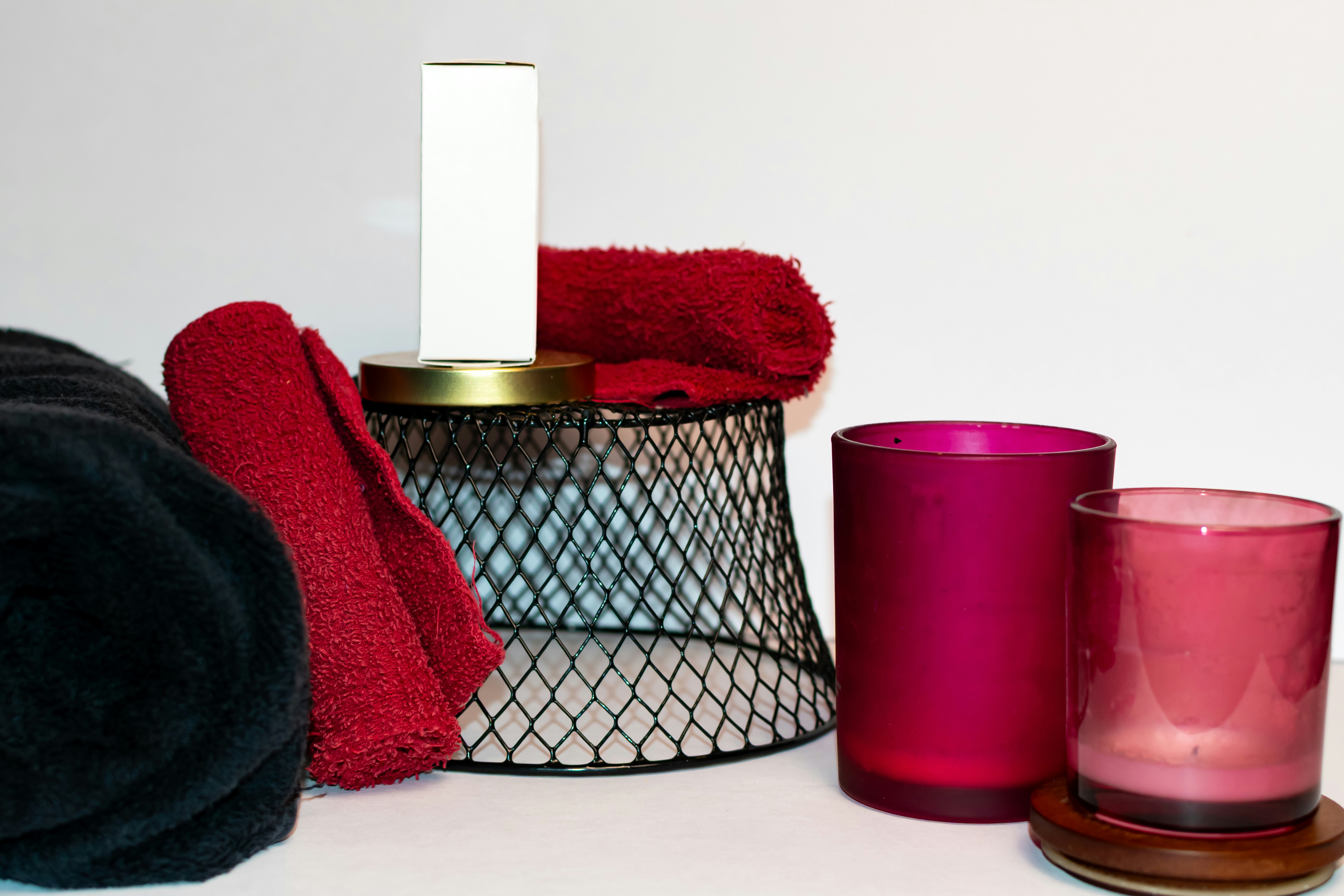 Assorted red and black candles and towels arranged around a wire basket on a white background.