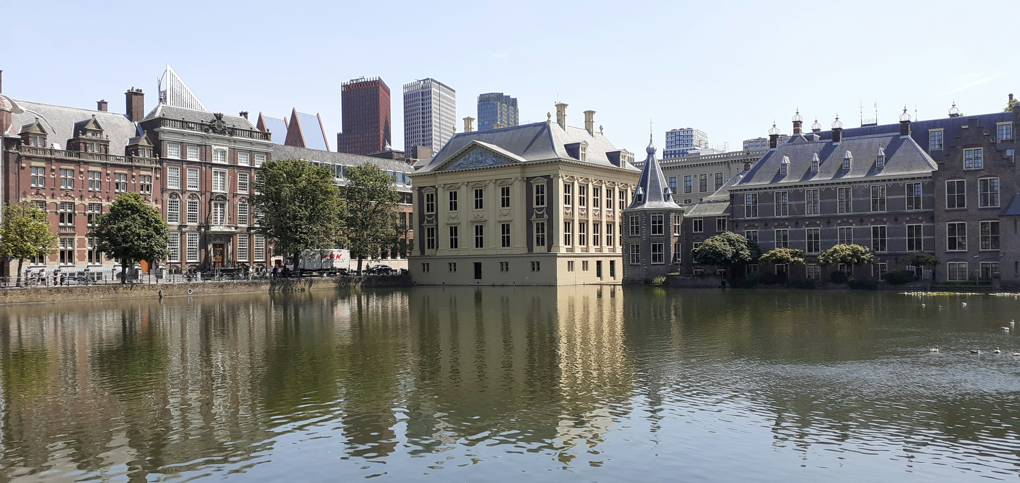 Historic buildings reflected in a tranquil pond with modern skyscrapers in the background.