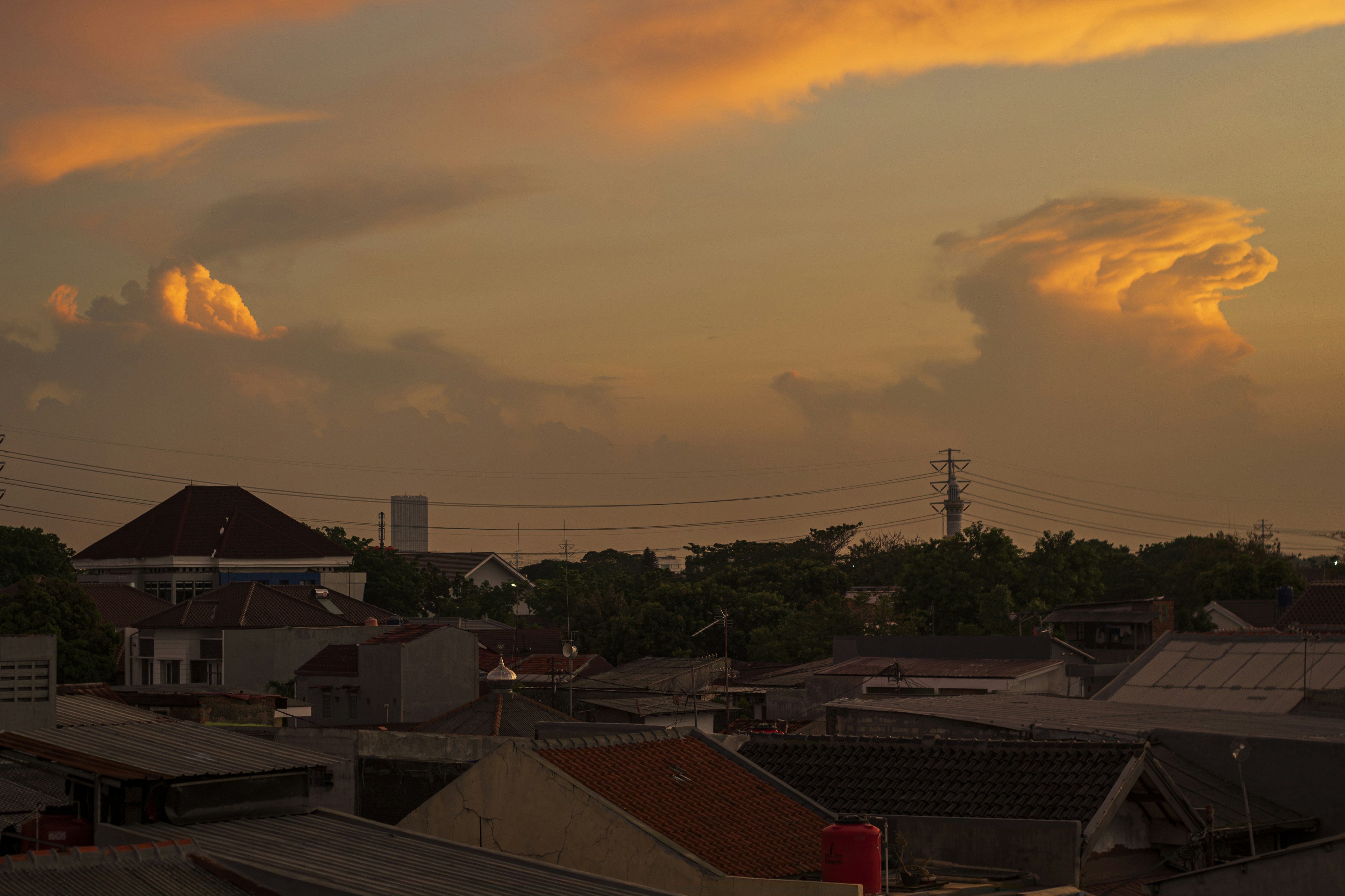 Sunset clouds illuminated in orange hues above rooftops and distant trees.