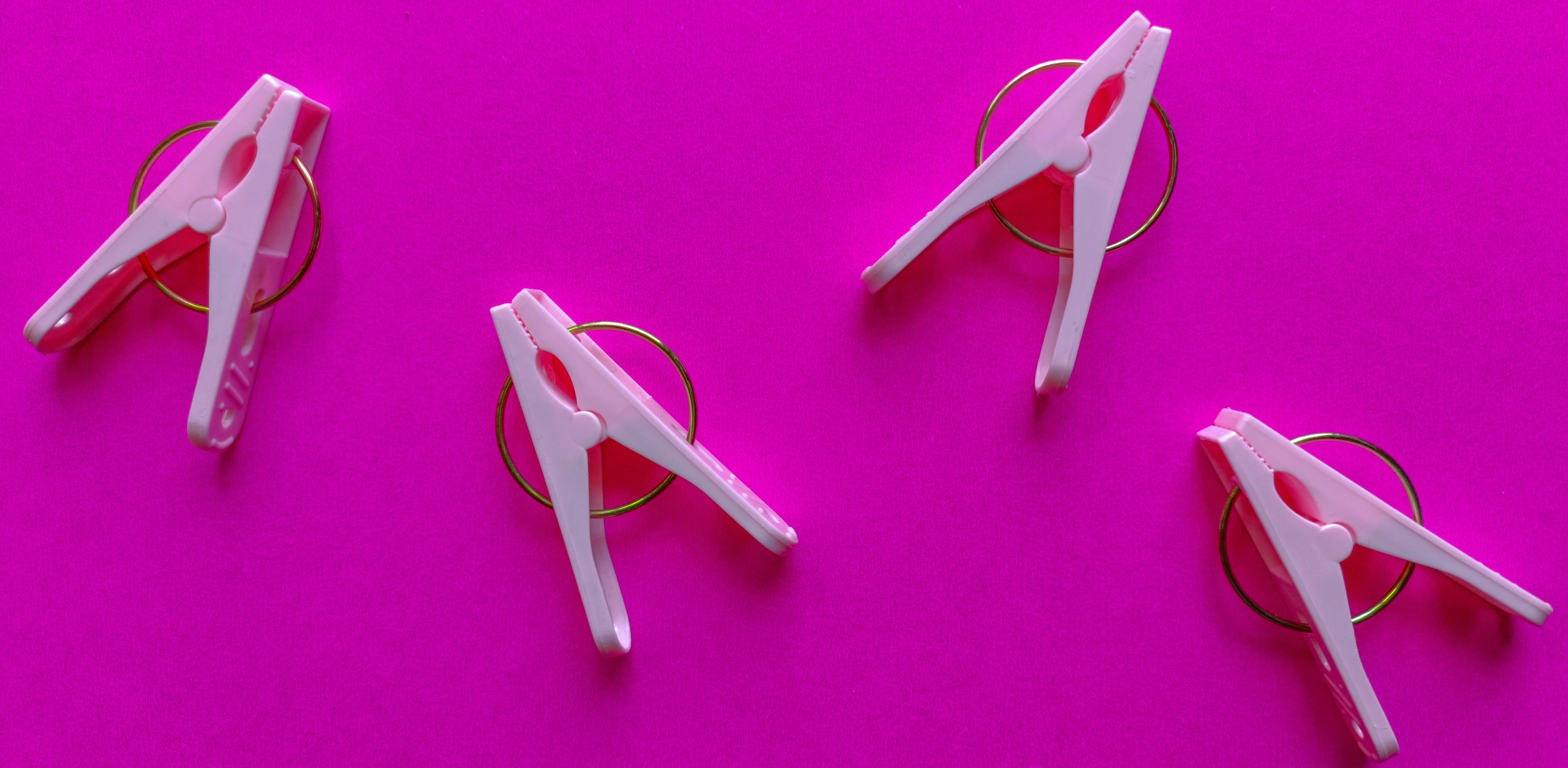 Minimalist still-life photograph of four white clothespins arranged on a magenta pink background.
