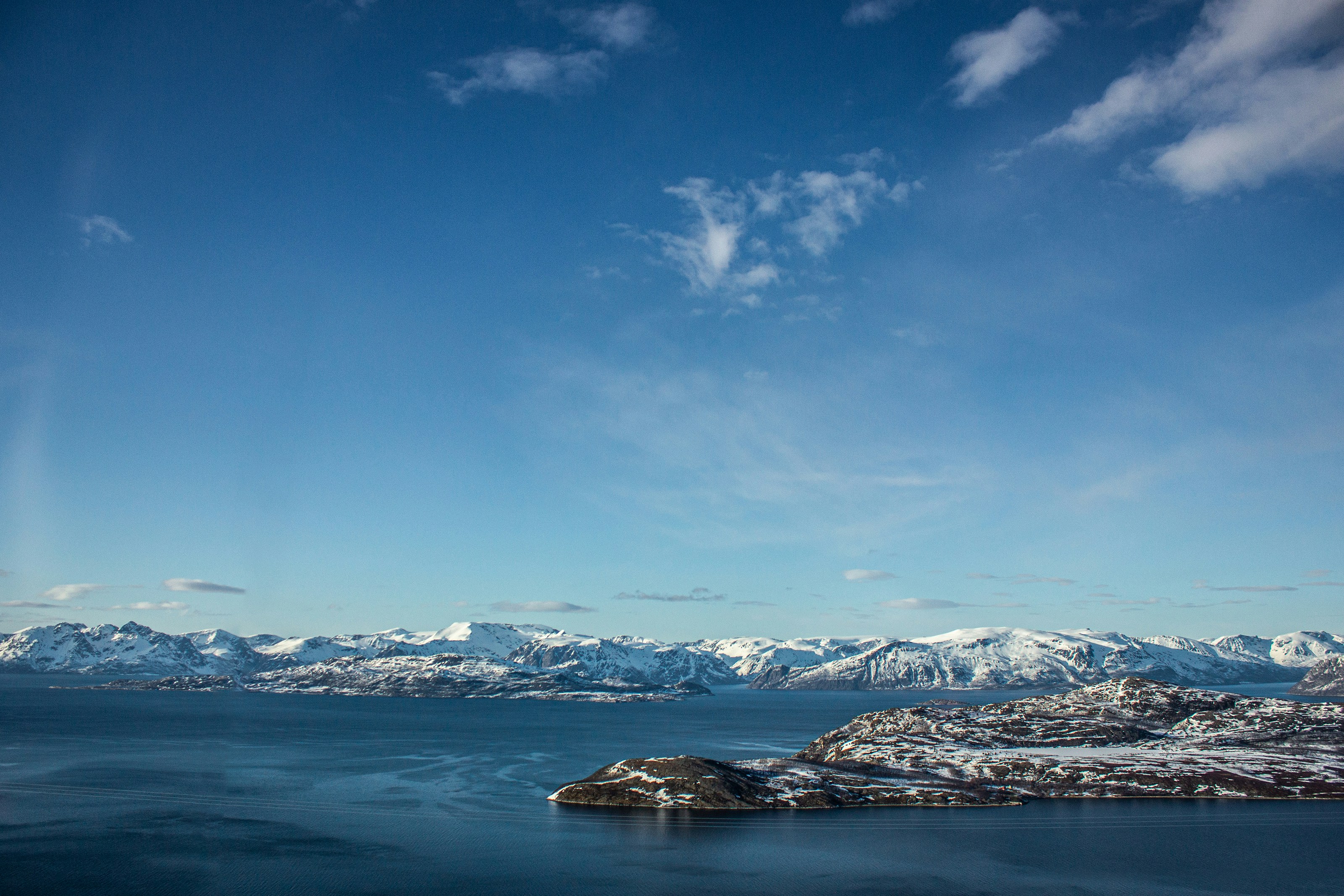 Snow-capped mountains meet a calm, expansive sea under a clear blue sky.