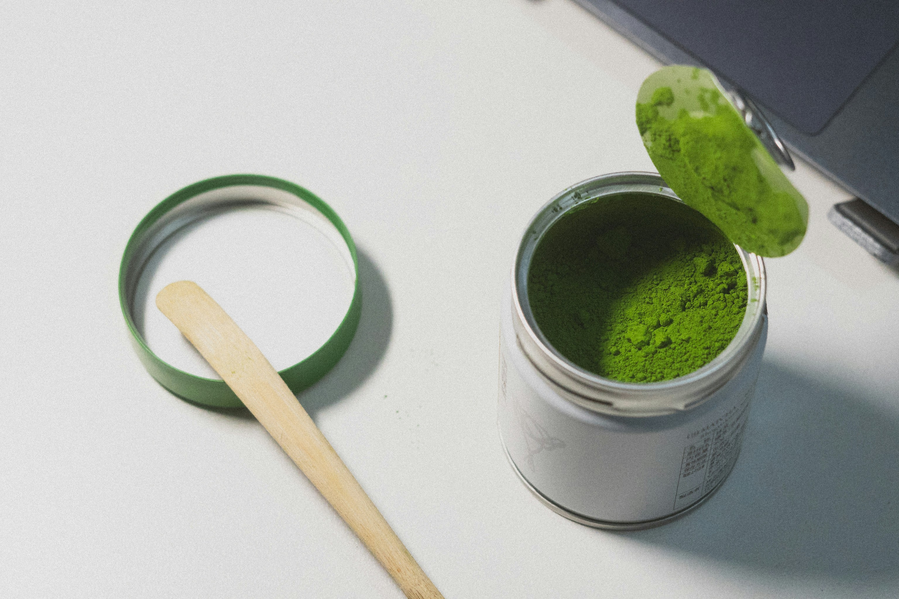 Verdant Vessel on White: Close-Up of a Matcha Jar and Wooden Spoon