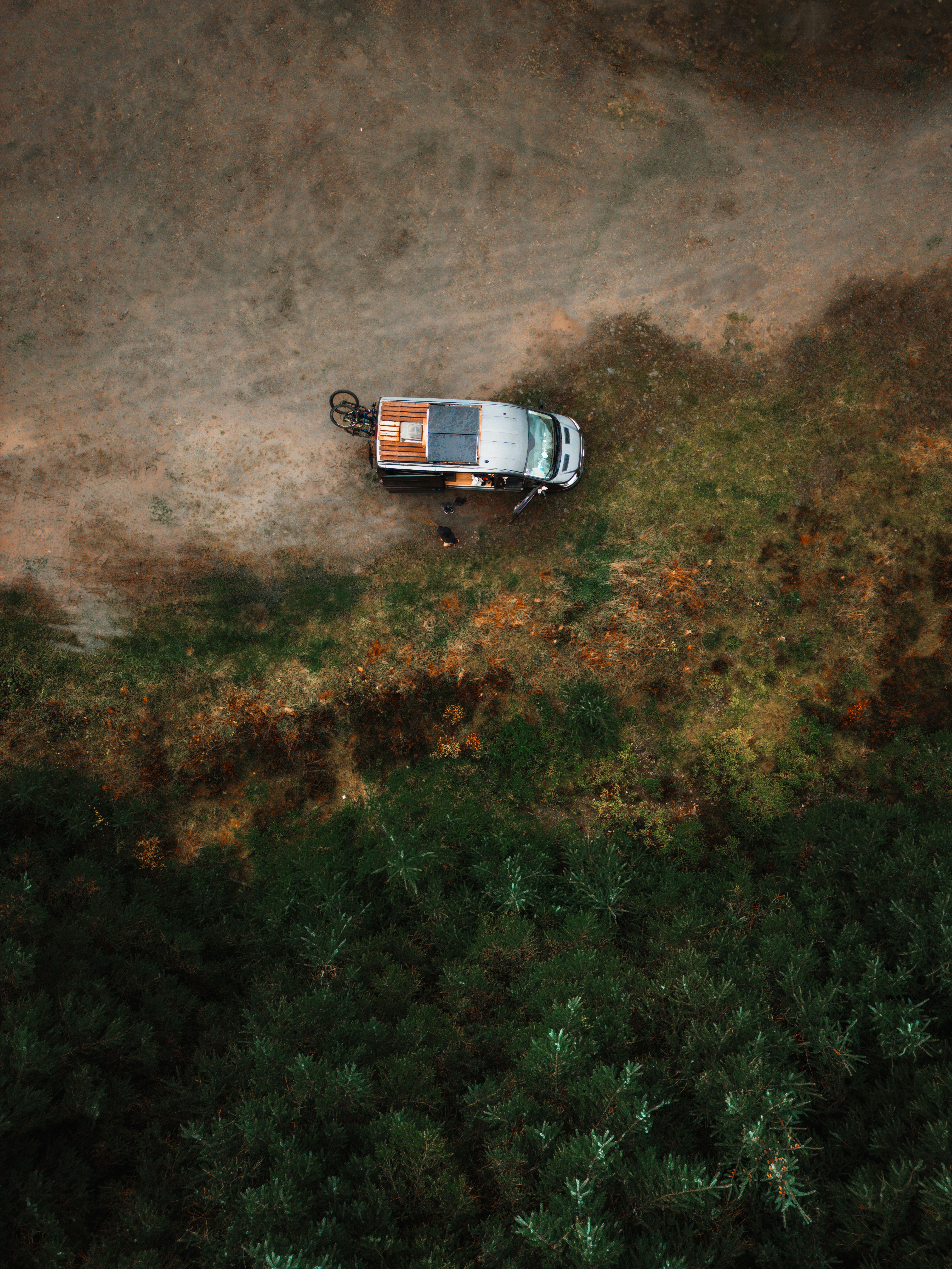 A van parked on a dirt path at the boundary of a lush forest.