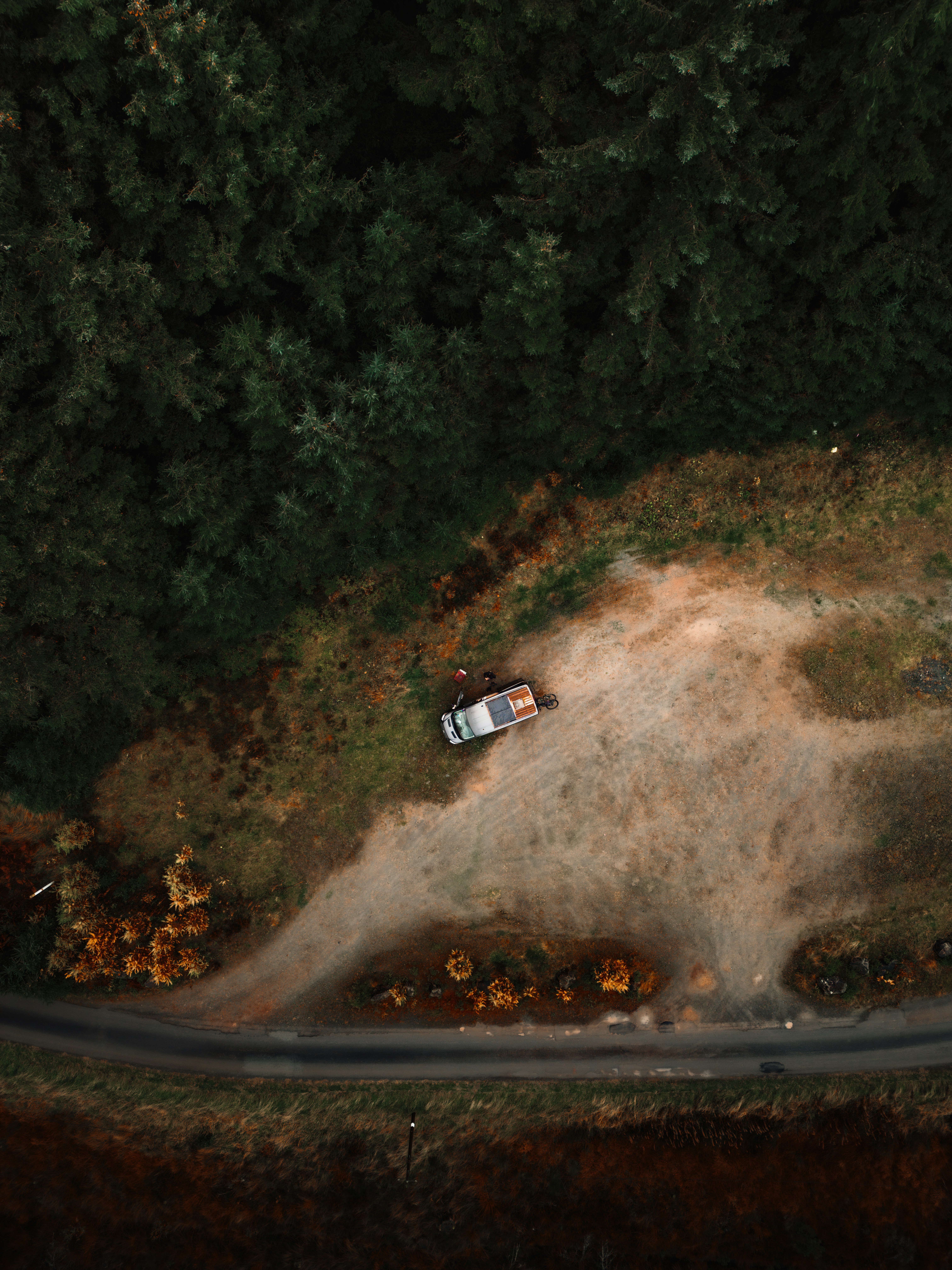Aerial view of a lone vehicle parked on a clearing surrounded by dense forest.