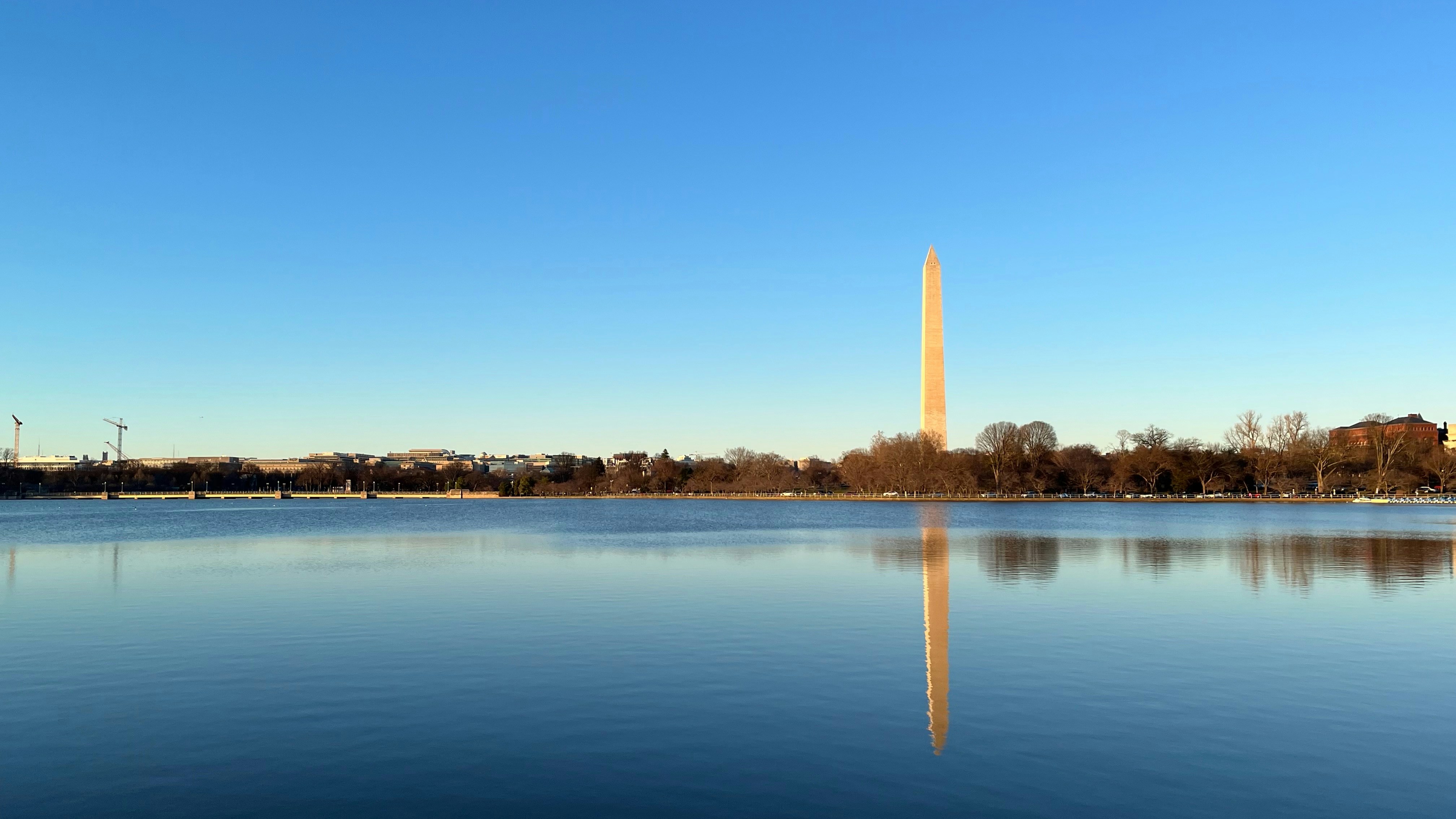 Washington Monument towering over a calm reflecting pool under a clear blue sky.