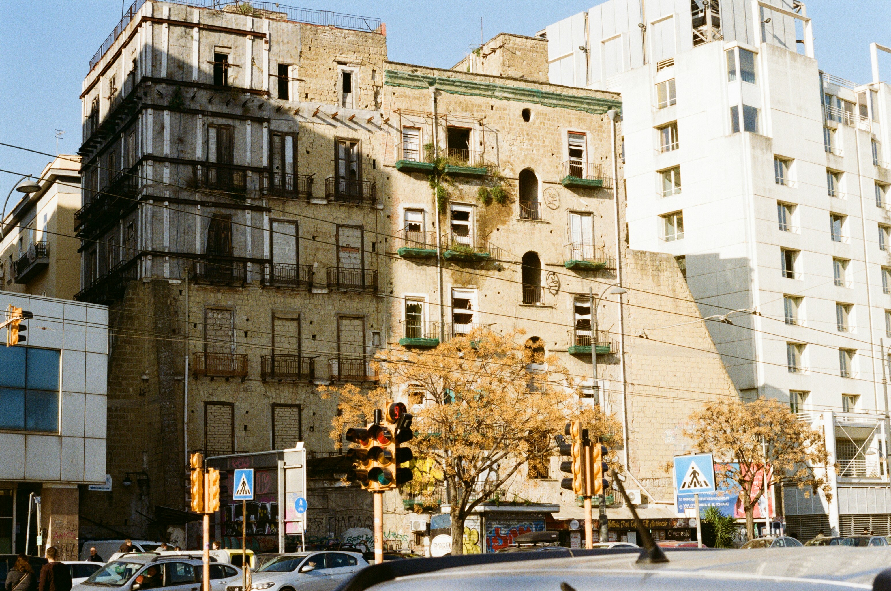 Weathered building facade with contrasting new architecture in a sunlit urban street.