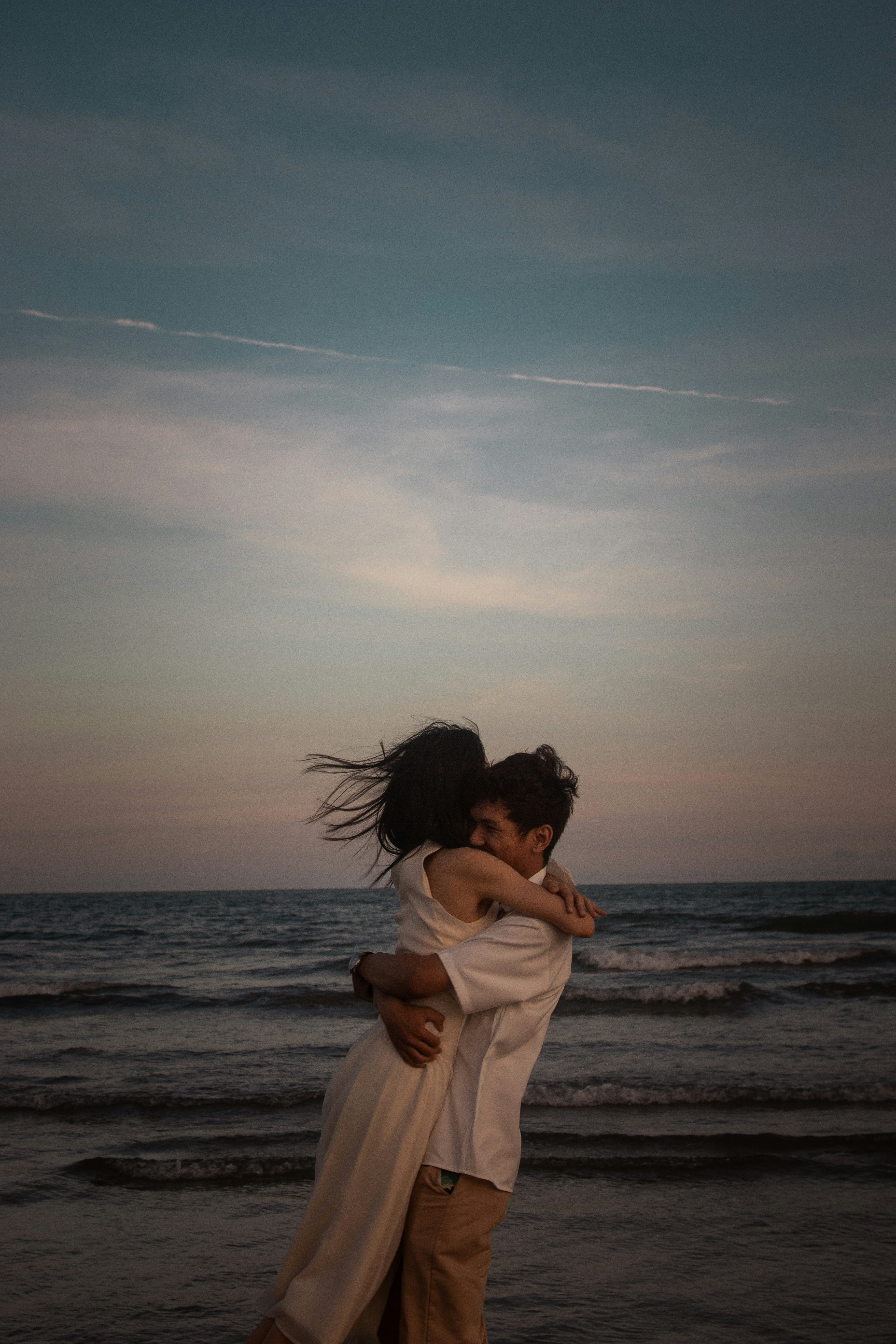 Couple embracing on a beach at sunset with waves in the background.