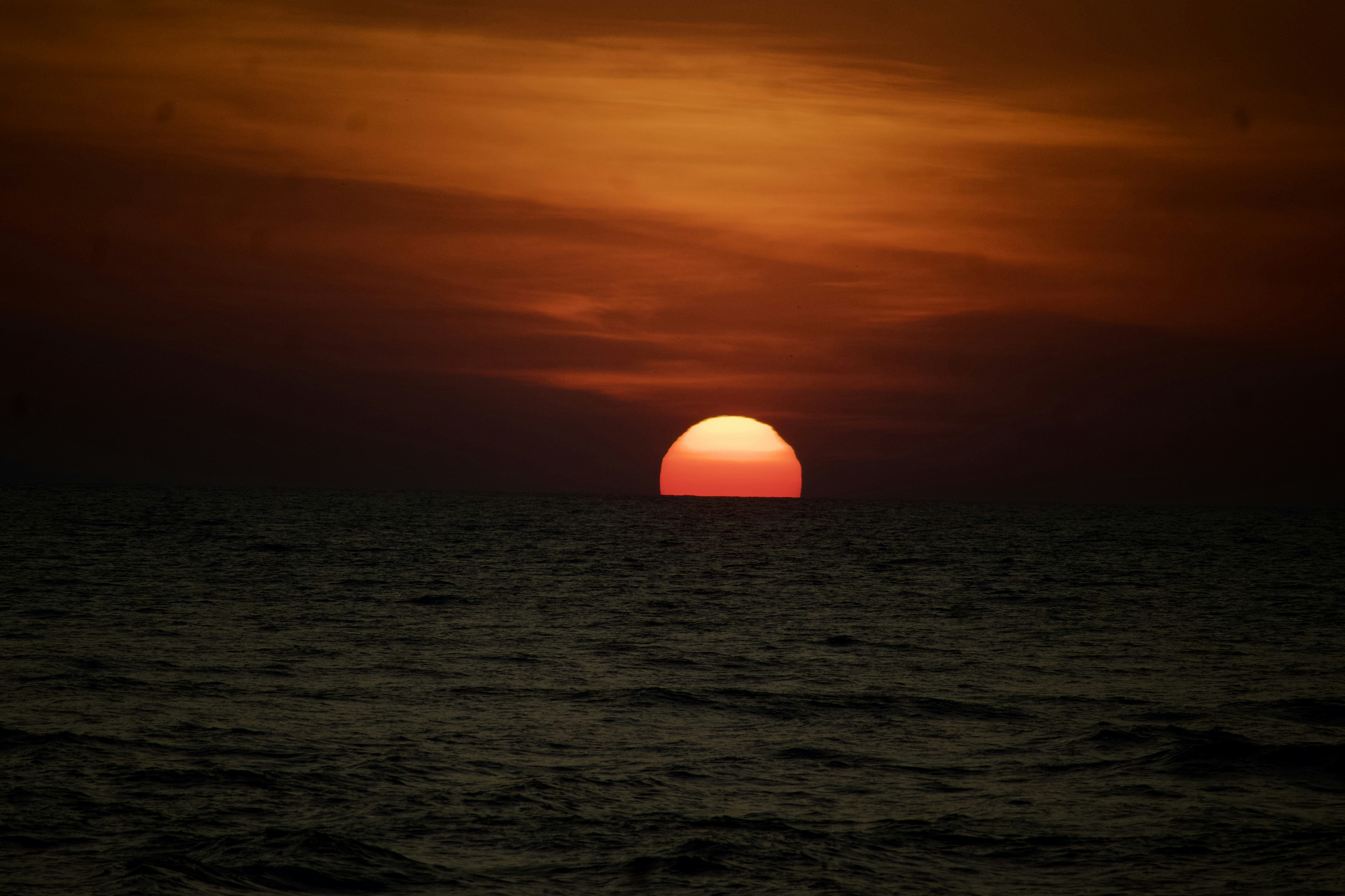 Vivid orange sun setting over a calm ocean under a richly colored sky.