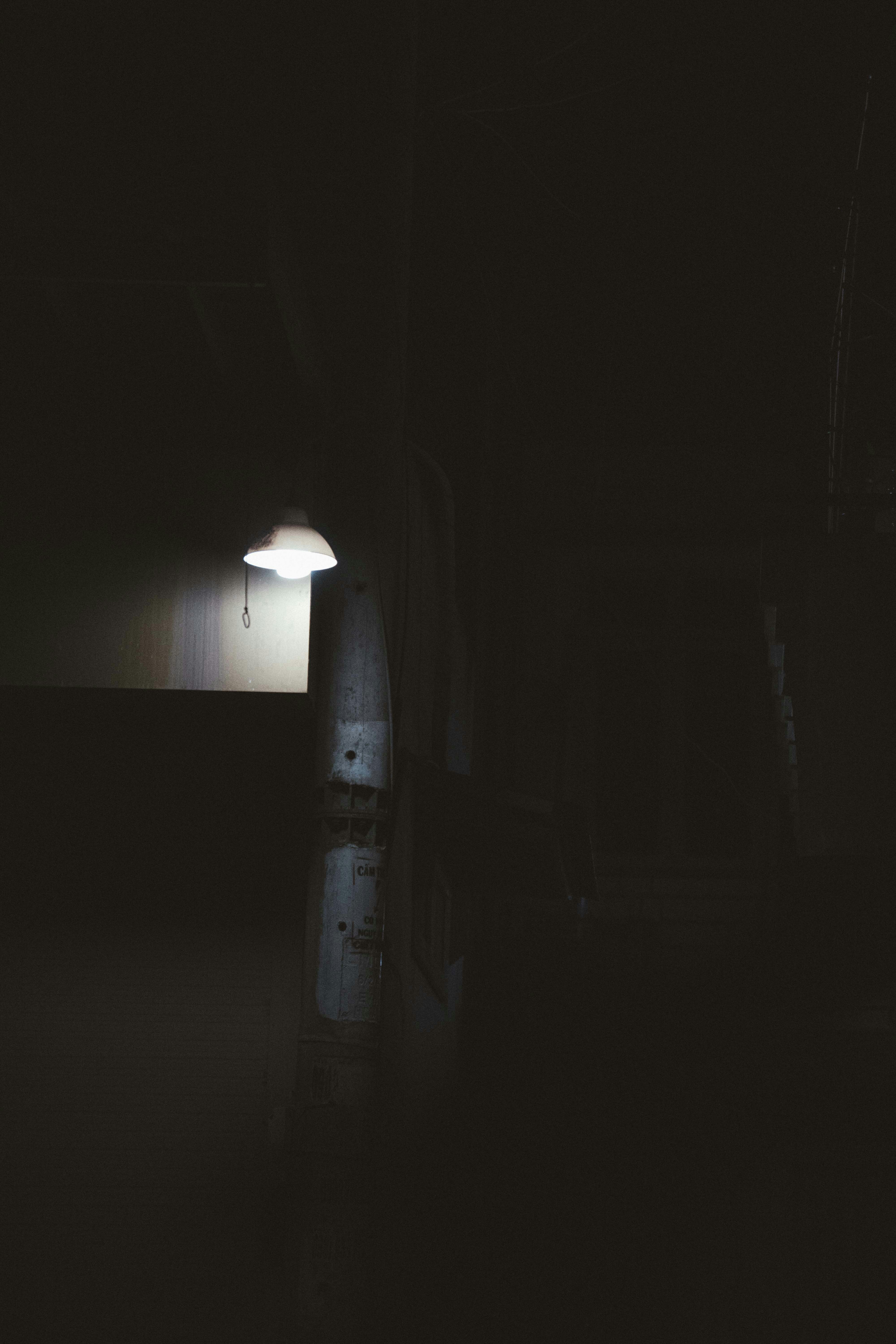 A solitary light bulb hangs in a dimly lit space, casting a soft glow amidst shadows and industrial elements.