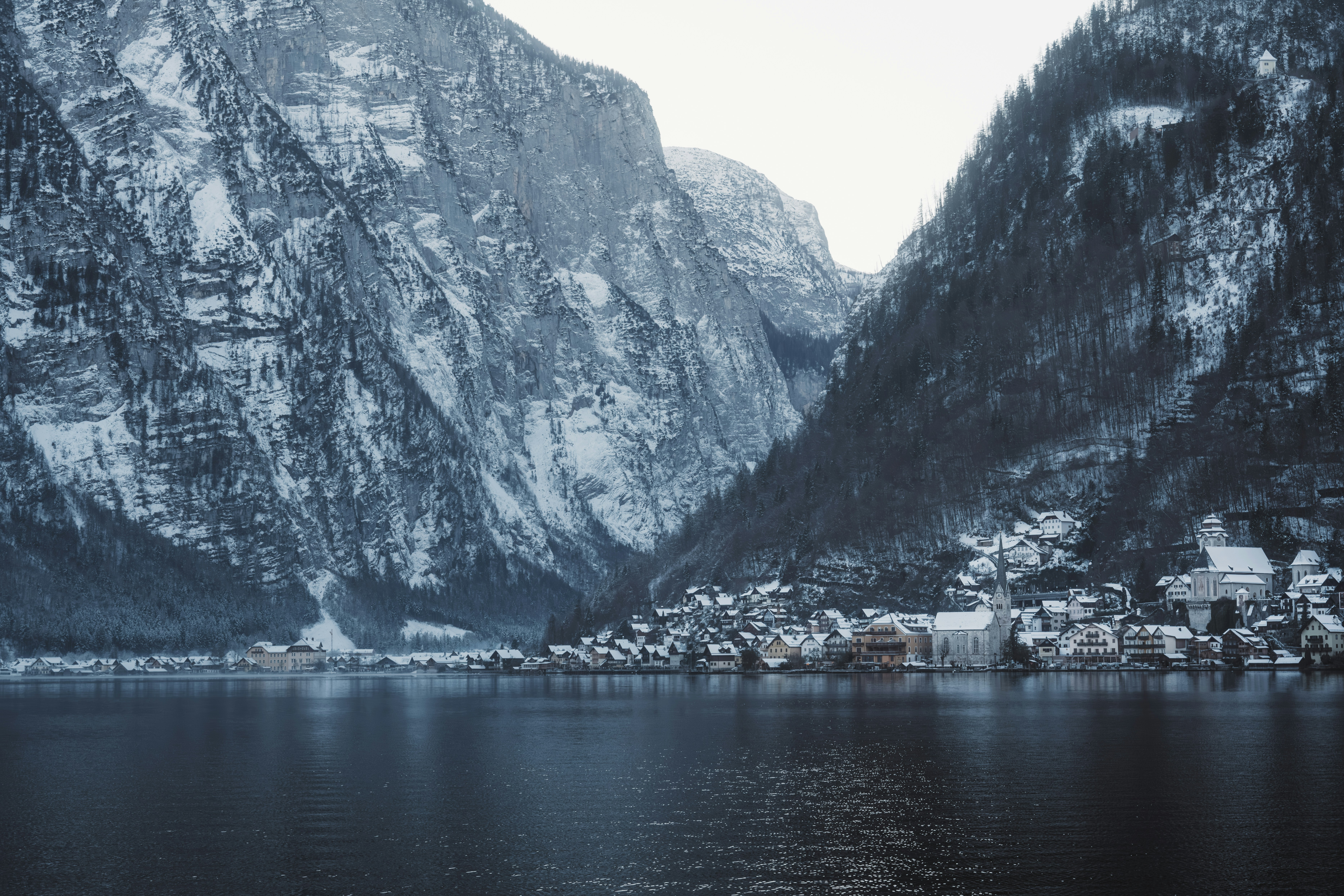 Snow-dusted village nestled between towering mountains along a tranquil lake.
