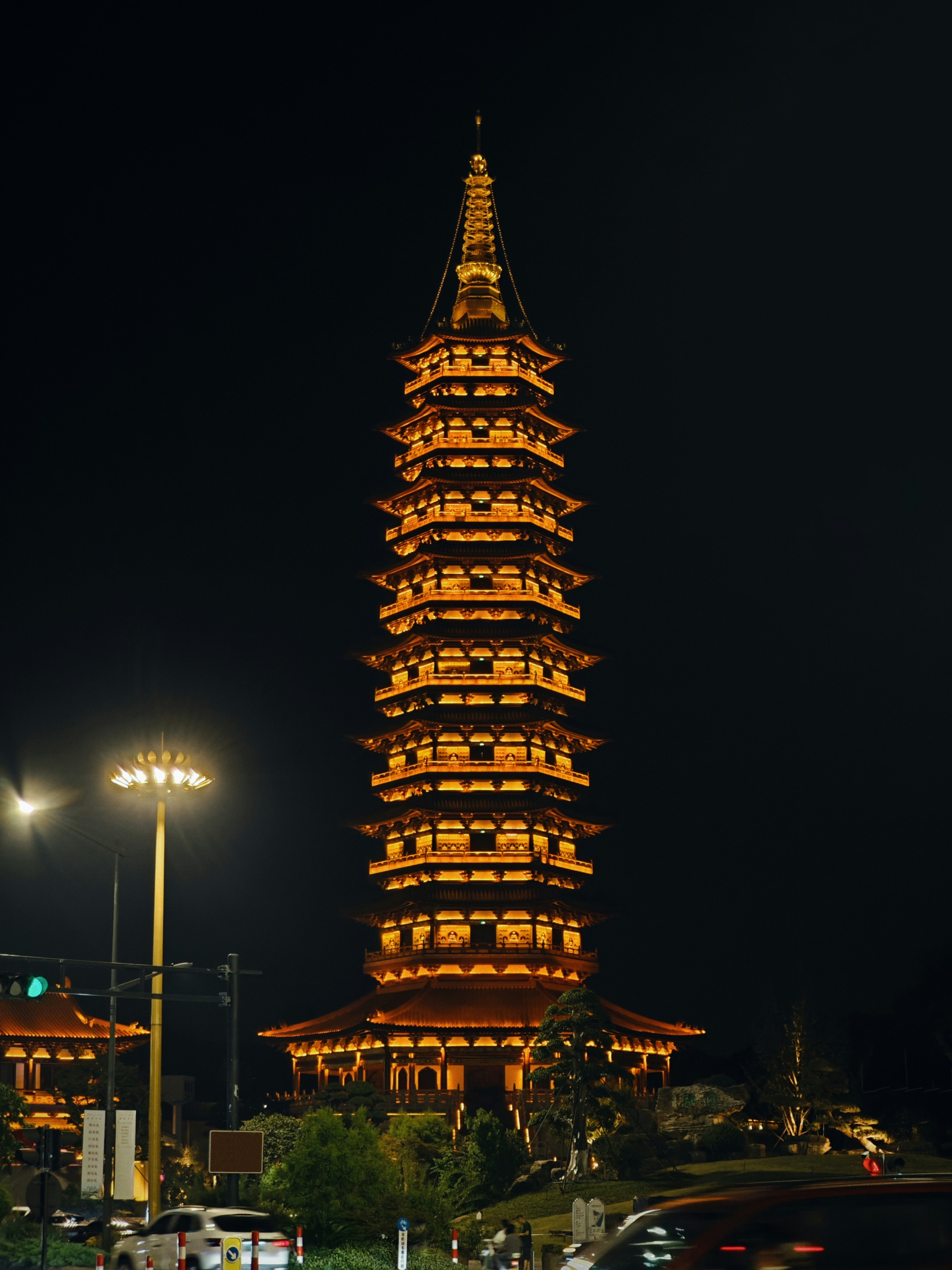 Night photograph of a nine-story pagoda illuminated in amber light against a dark sky, with street lamps and moving traffic in the foreground.