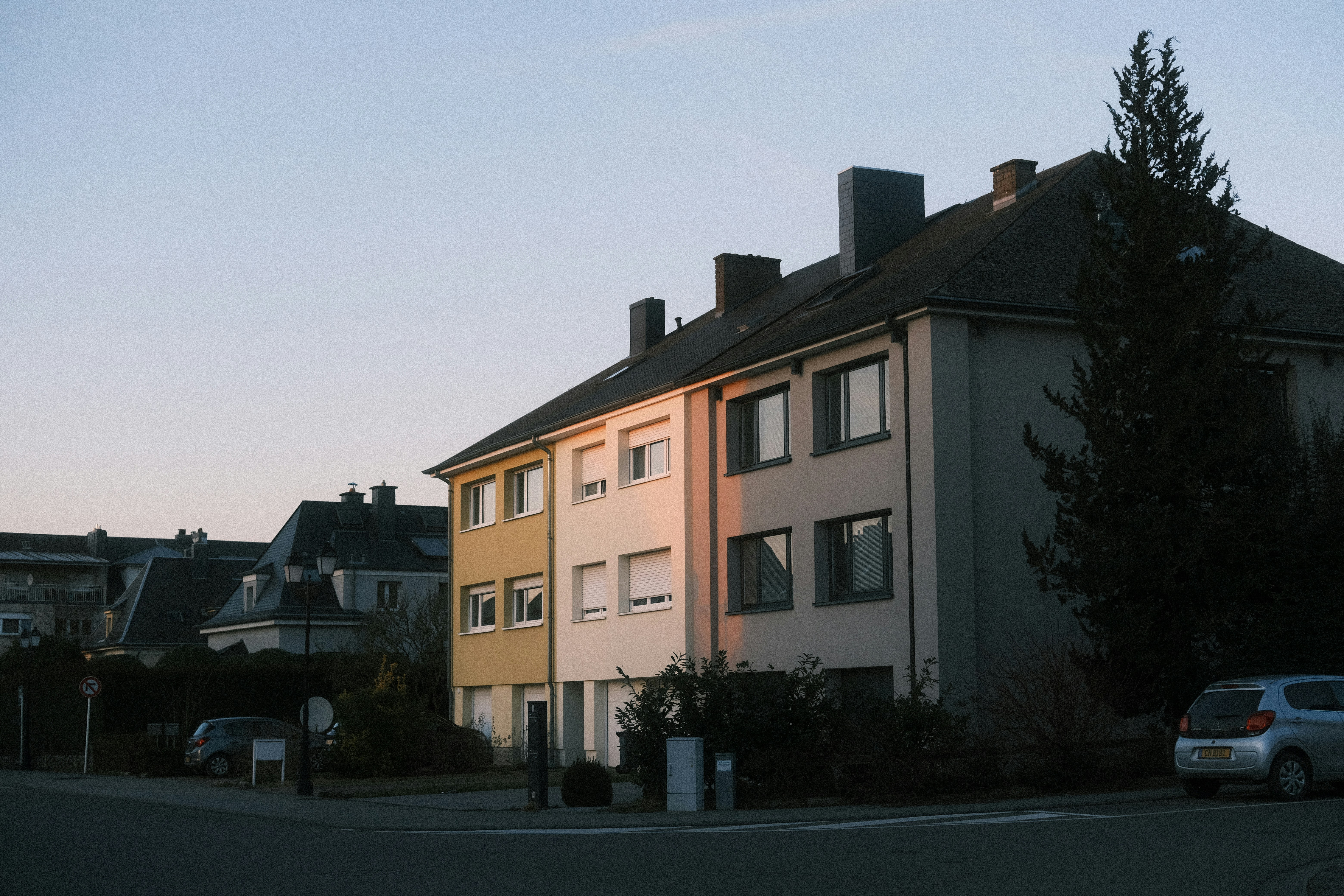 Sunset light casts a warm hue on a two-story building with a parked car nearby.