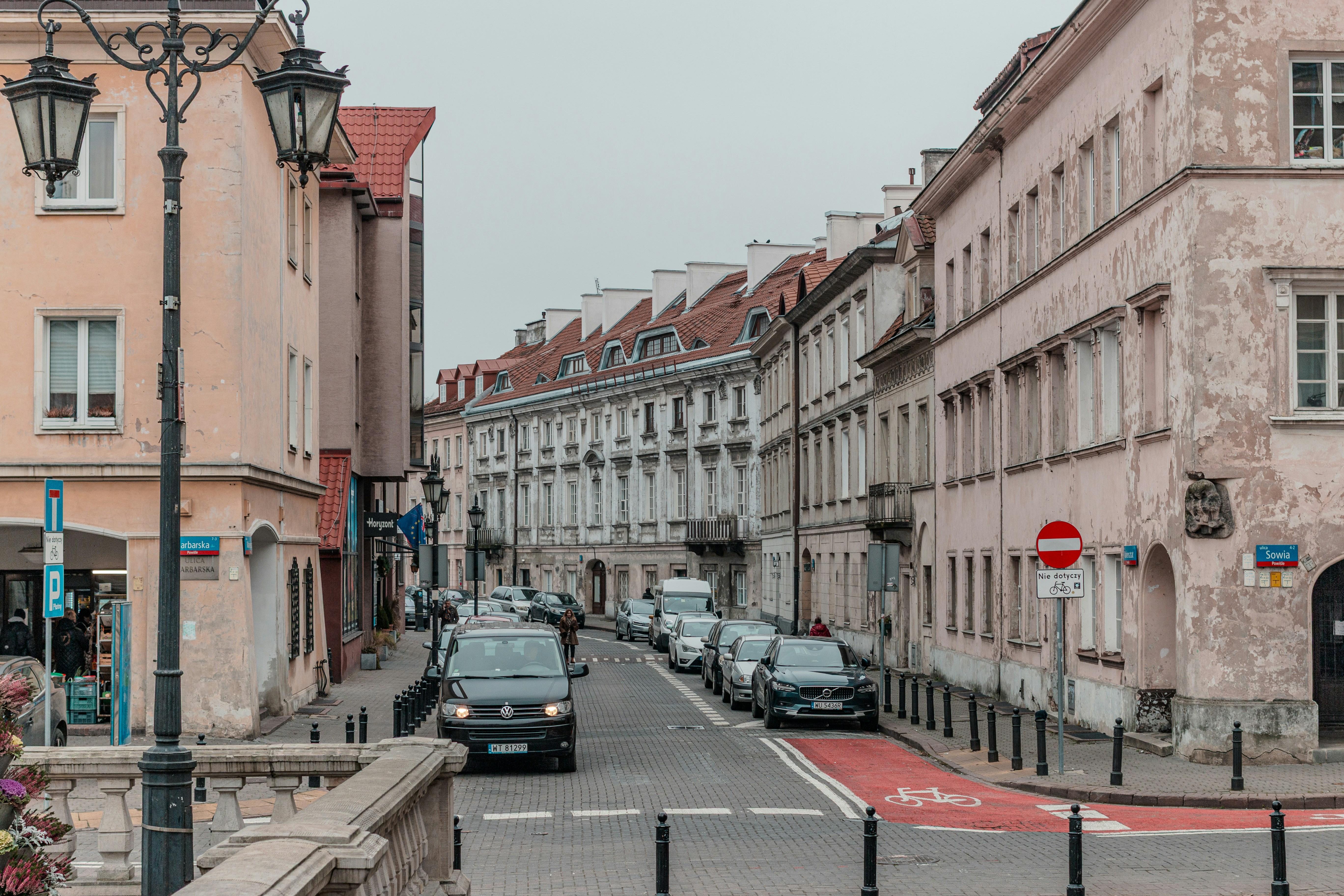 Historic European street lined with pastel buildings and parked cars under an overcast sky.