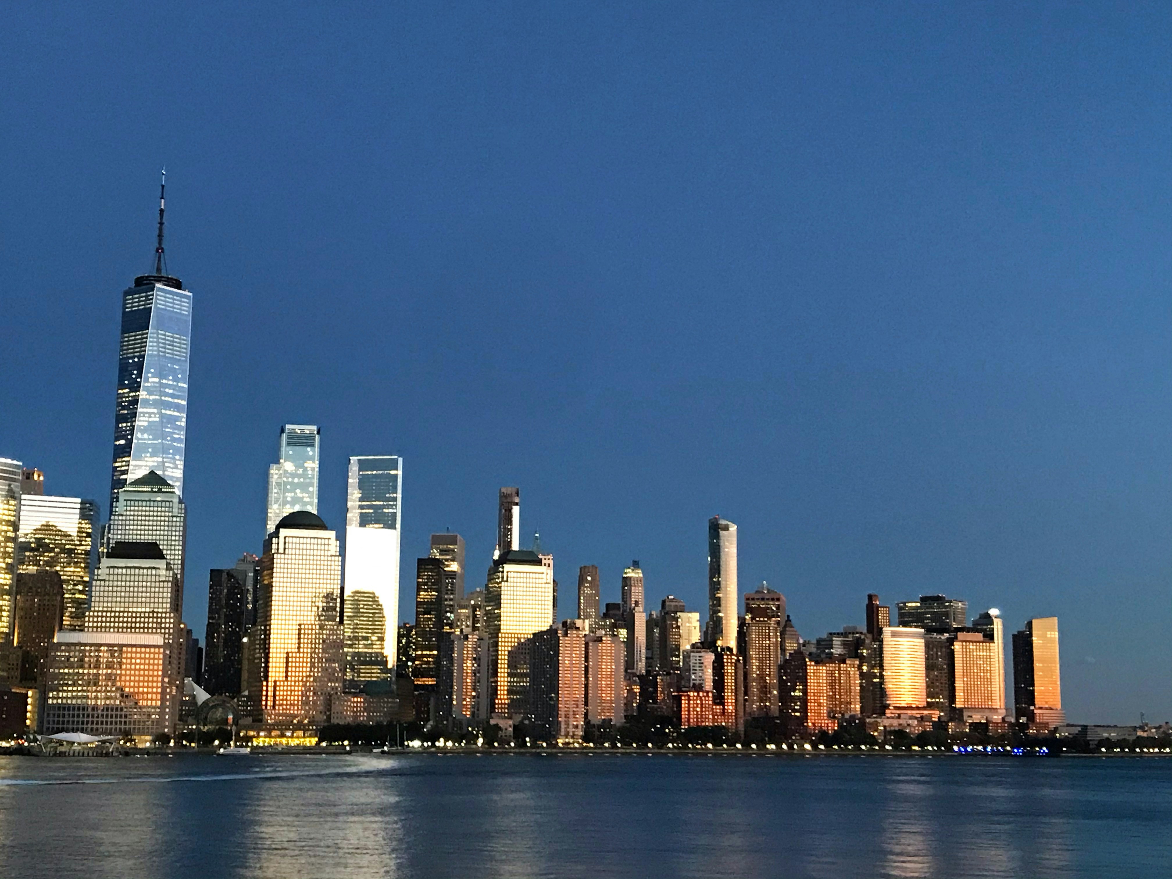 City skyline reflecting golden hues as dusk settles over calm waters.