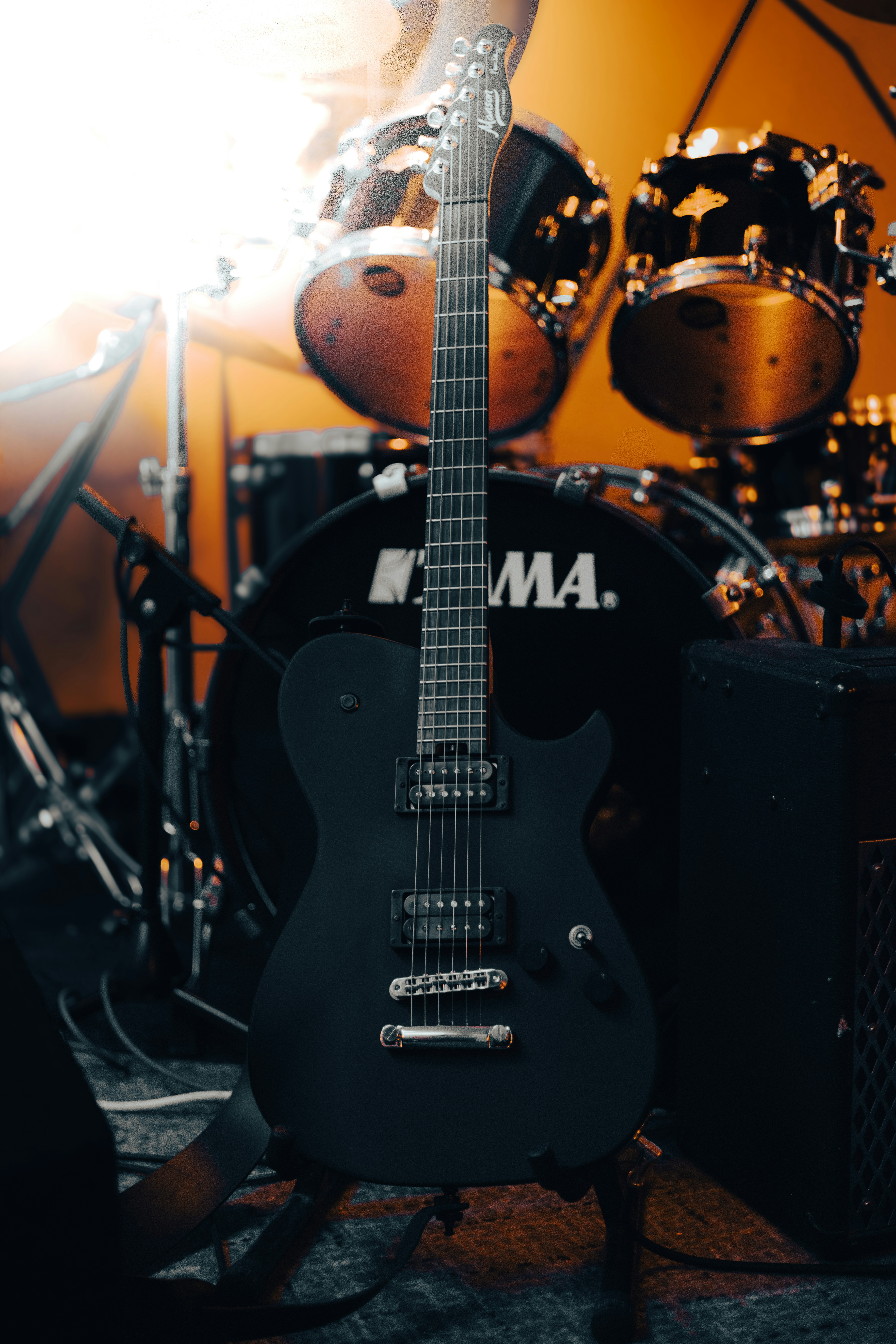Stage Quiet: A Black Solid-Body Guitar Amid Amber Drum Light