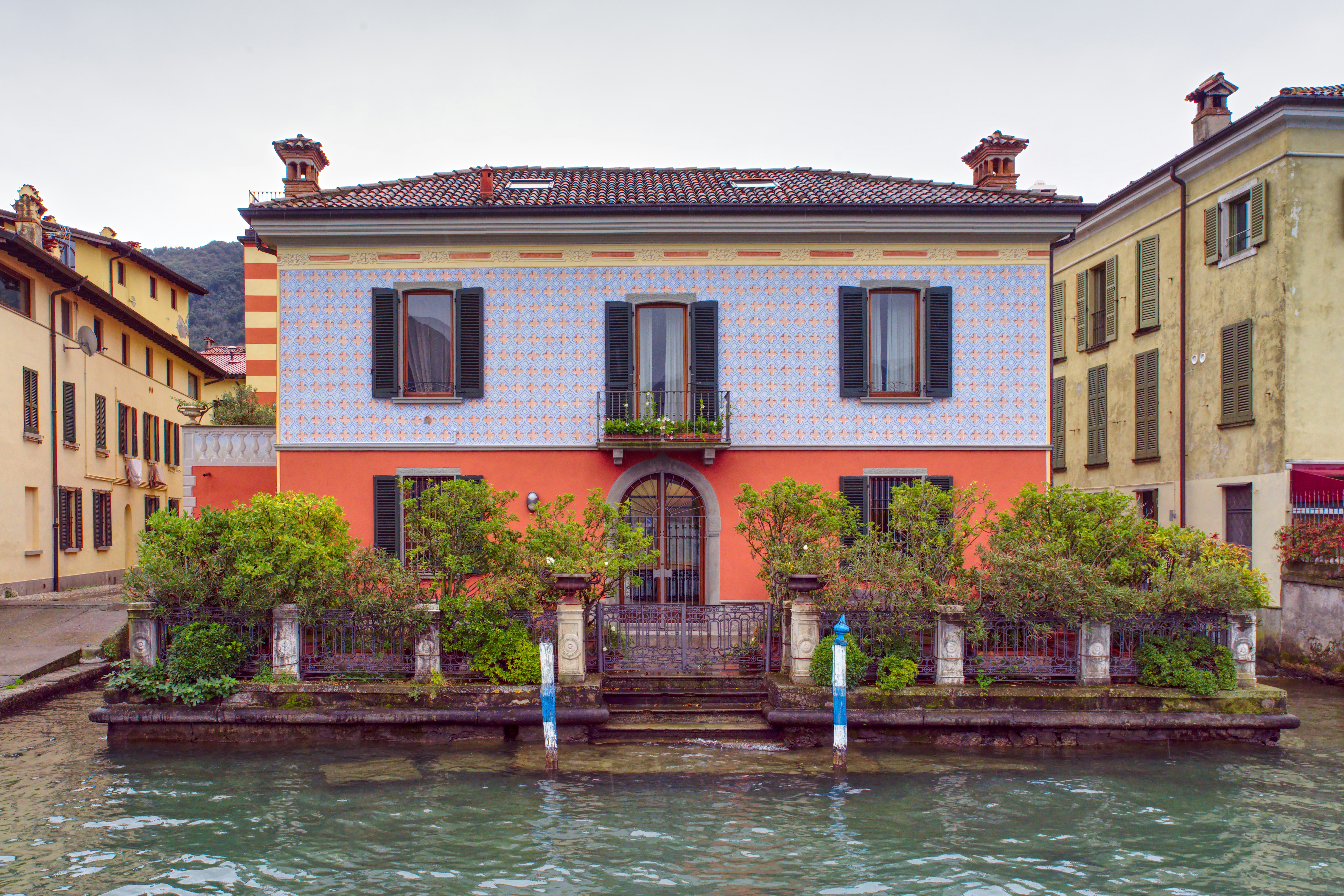 Colorful building with lush greenery on a canal's edge under an overcast sky.