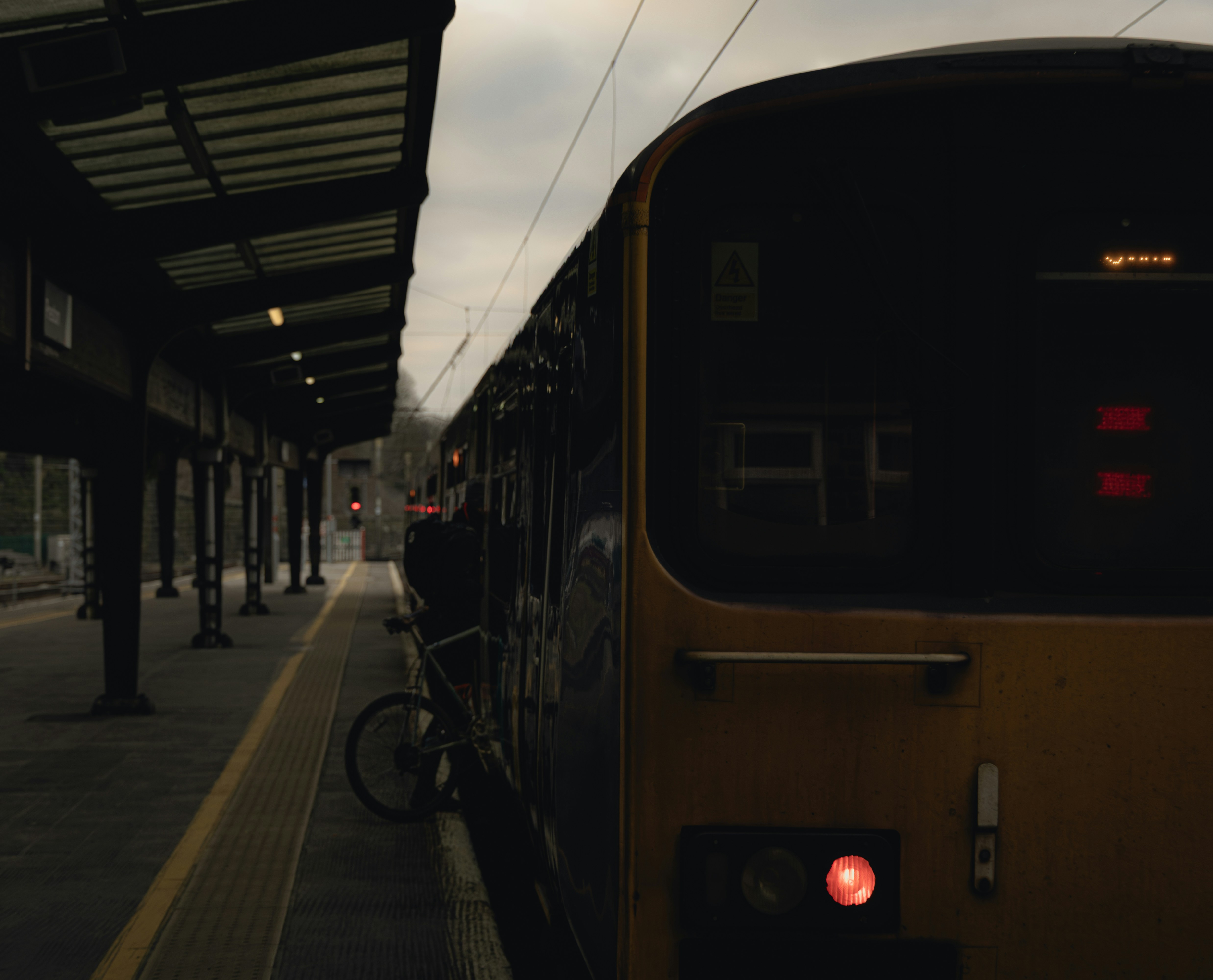 Cyclist with a bicycle boards a train on a dimly lit platform with glowing red lights.
