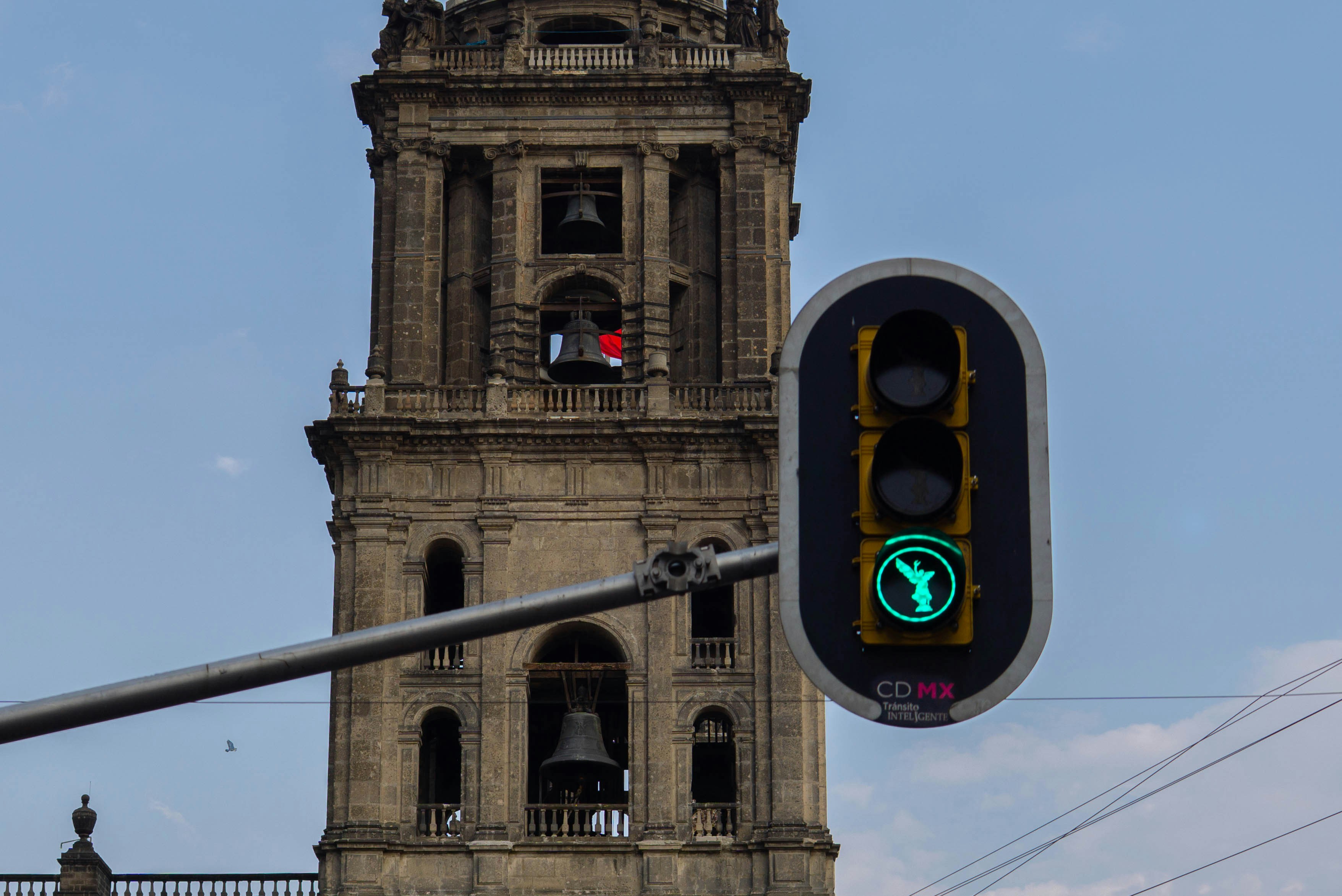 Traffic light against the backdrop of a historic stone tower under a clear blue sky.
