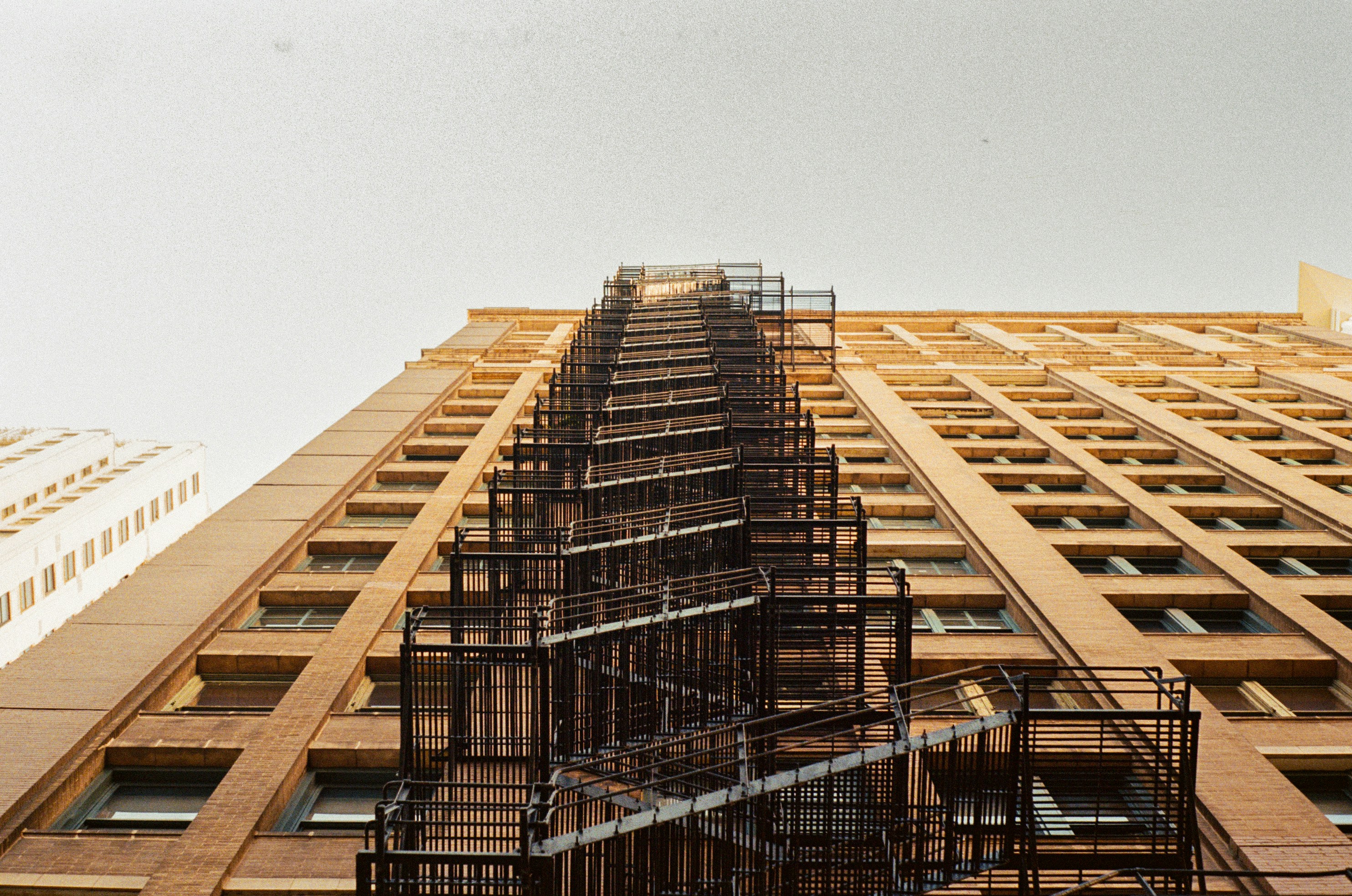 Zig-zagging fire escape climbs a tall brown brick building under a clear sky.