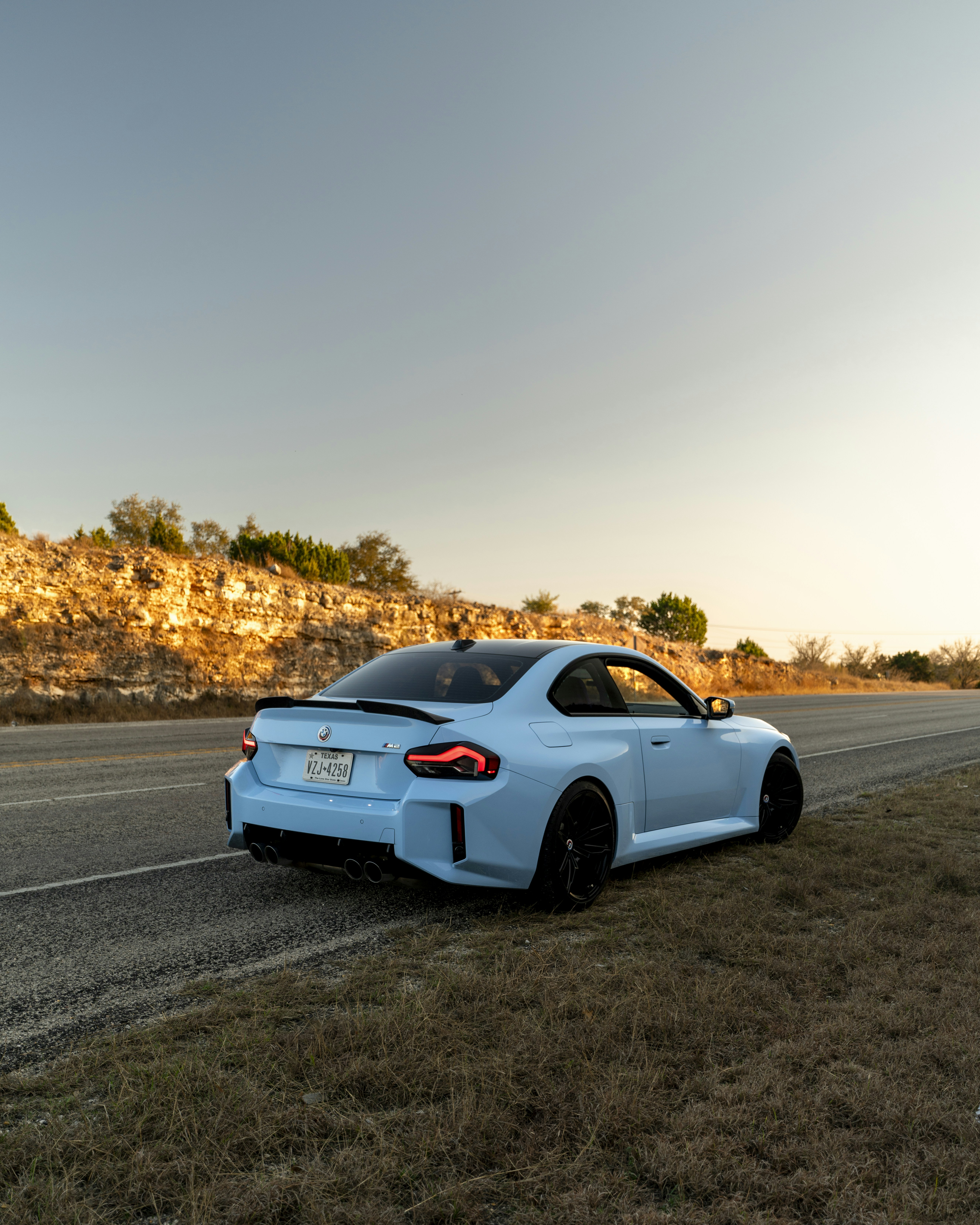 A blue car driving down a road next to a hill photo – Free Bmw Image on ...