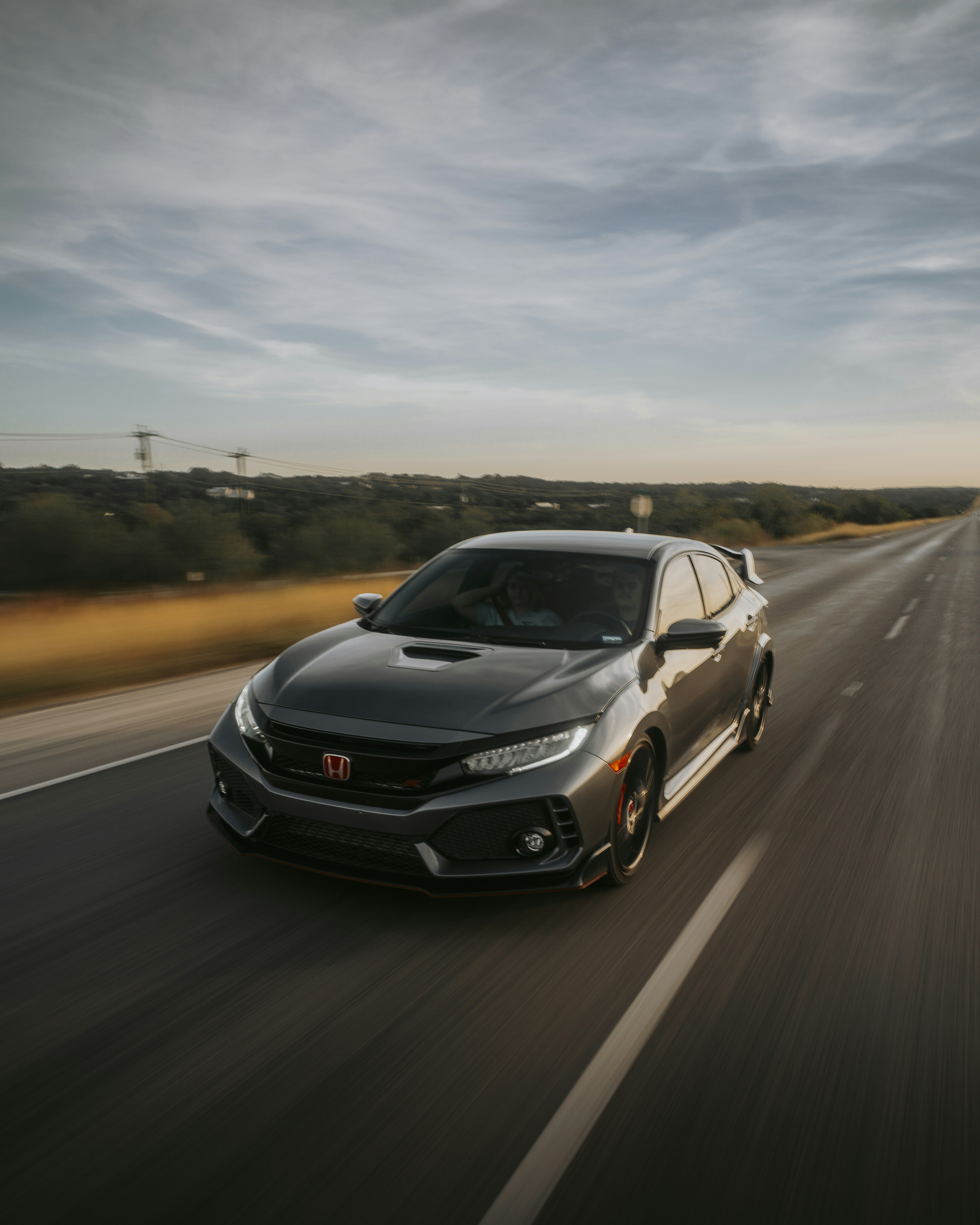 A black car driving down a highway next to a forest photo – Free Civic ...