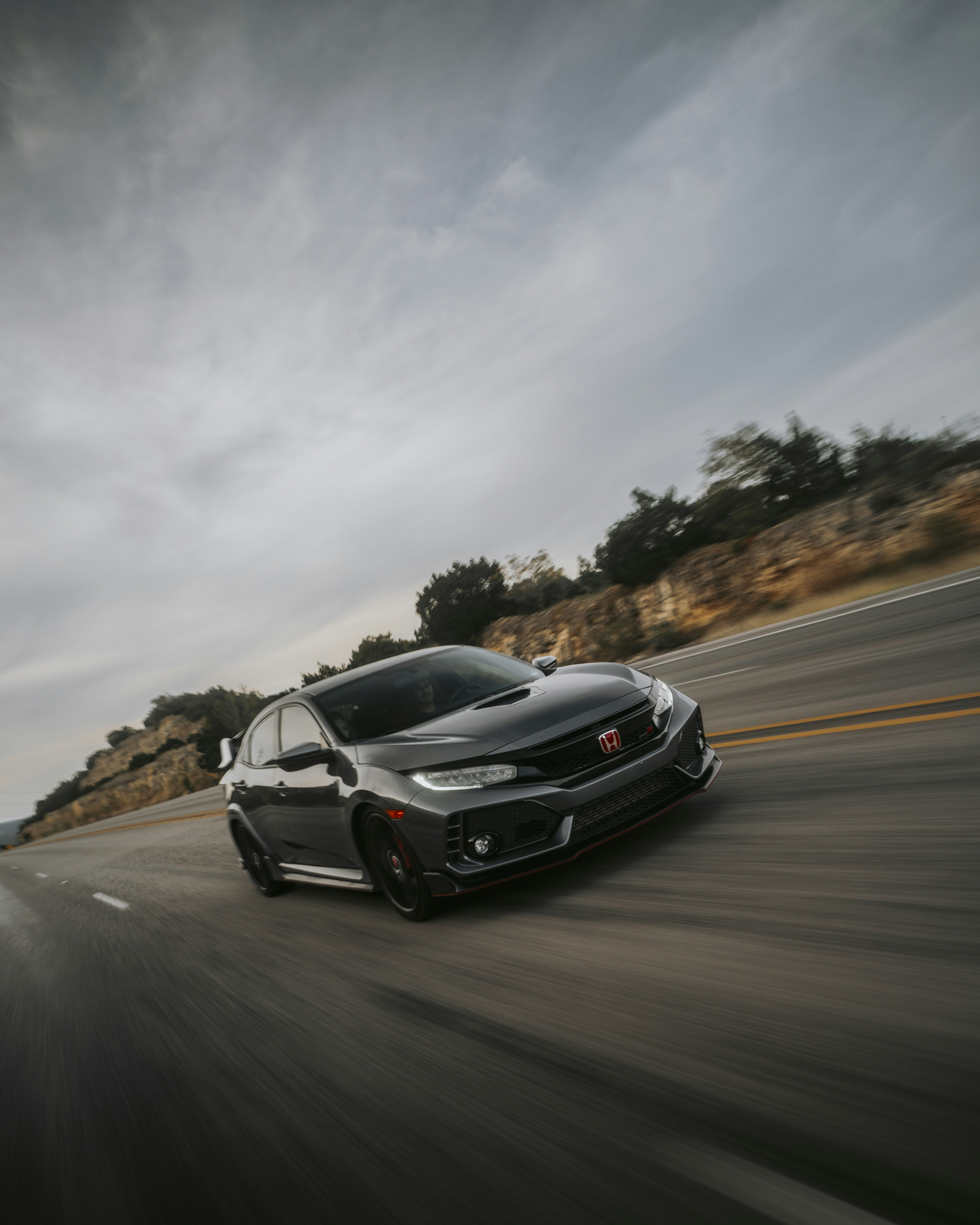 A black car driving down a road next to a hill photo – Free Civic type ...