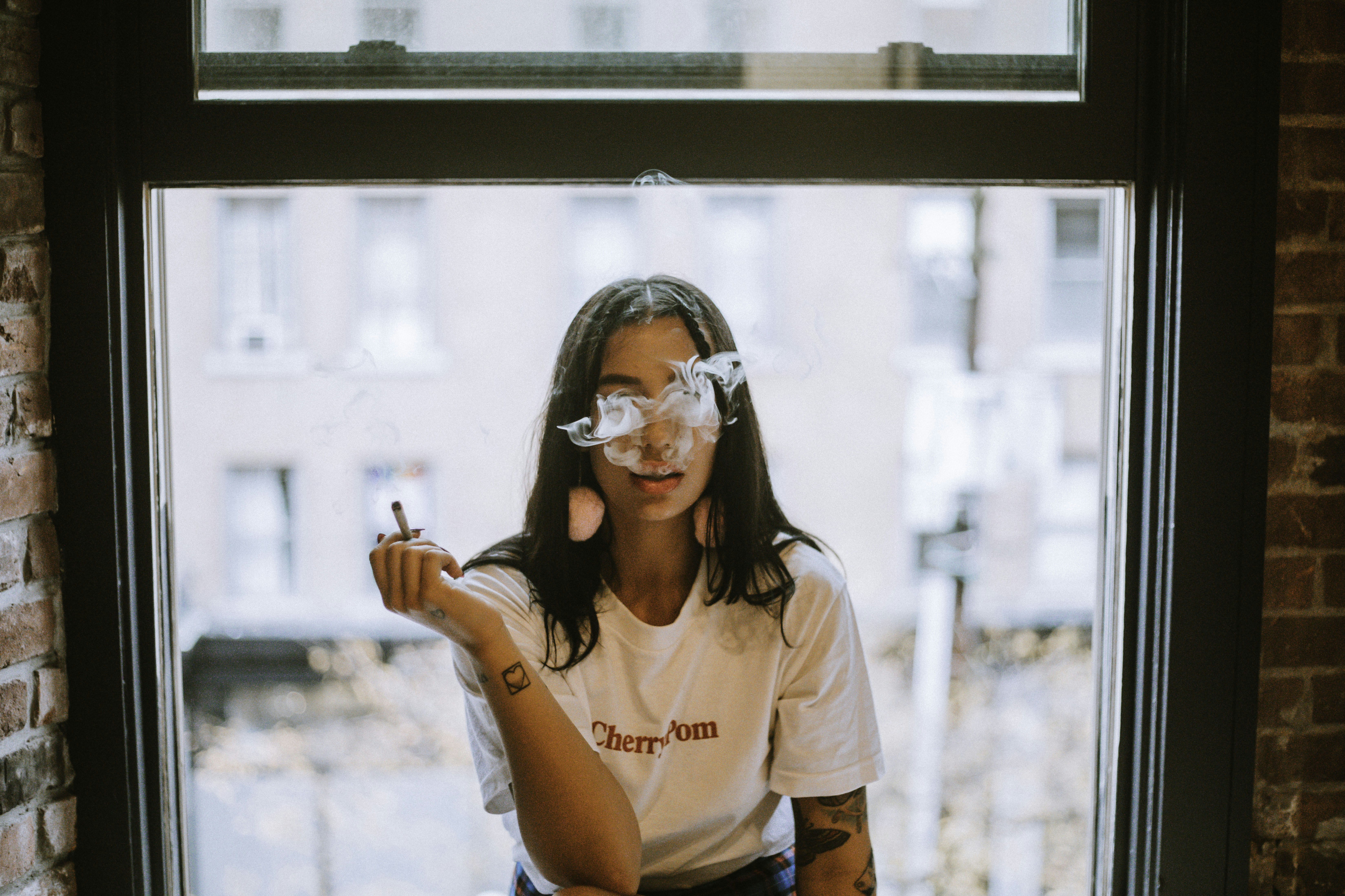 A woman smoking a cigarette in front of a window photo – Free Smoking ...