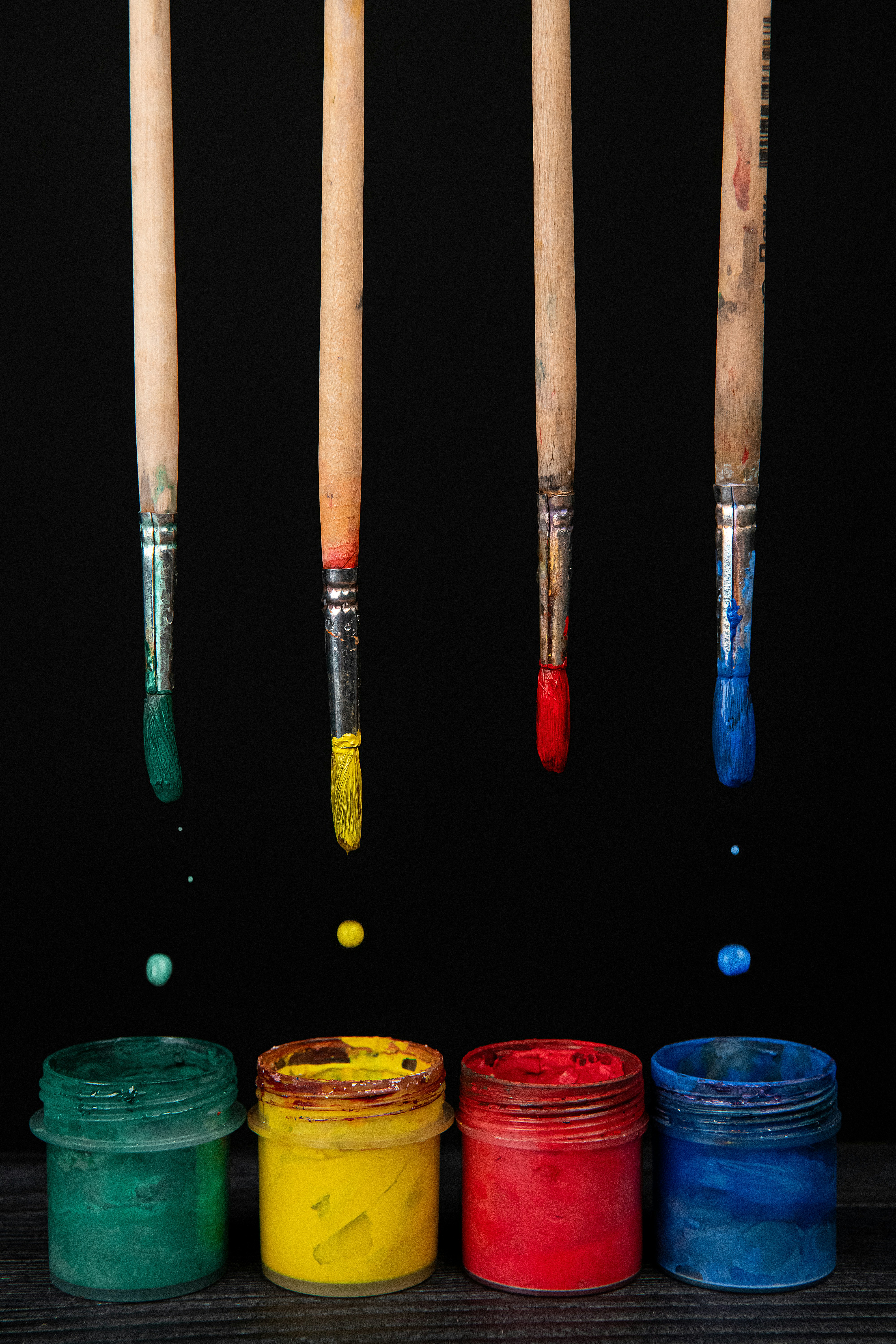 Hanging Hues: Four Brush Tips Above a Primary Palette