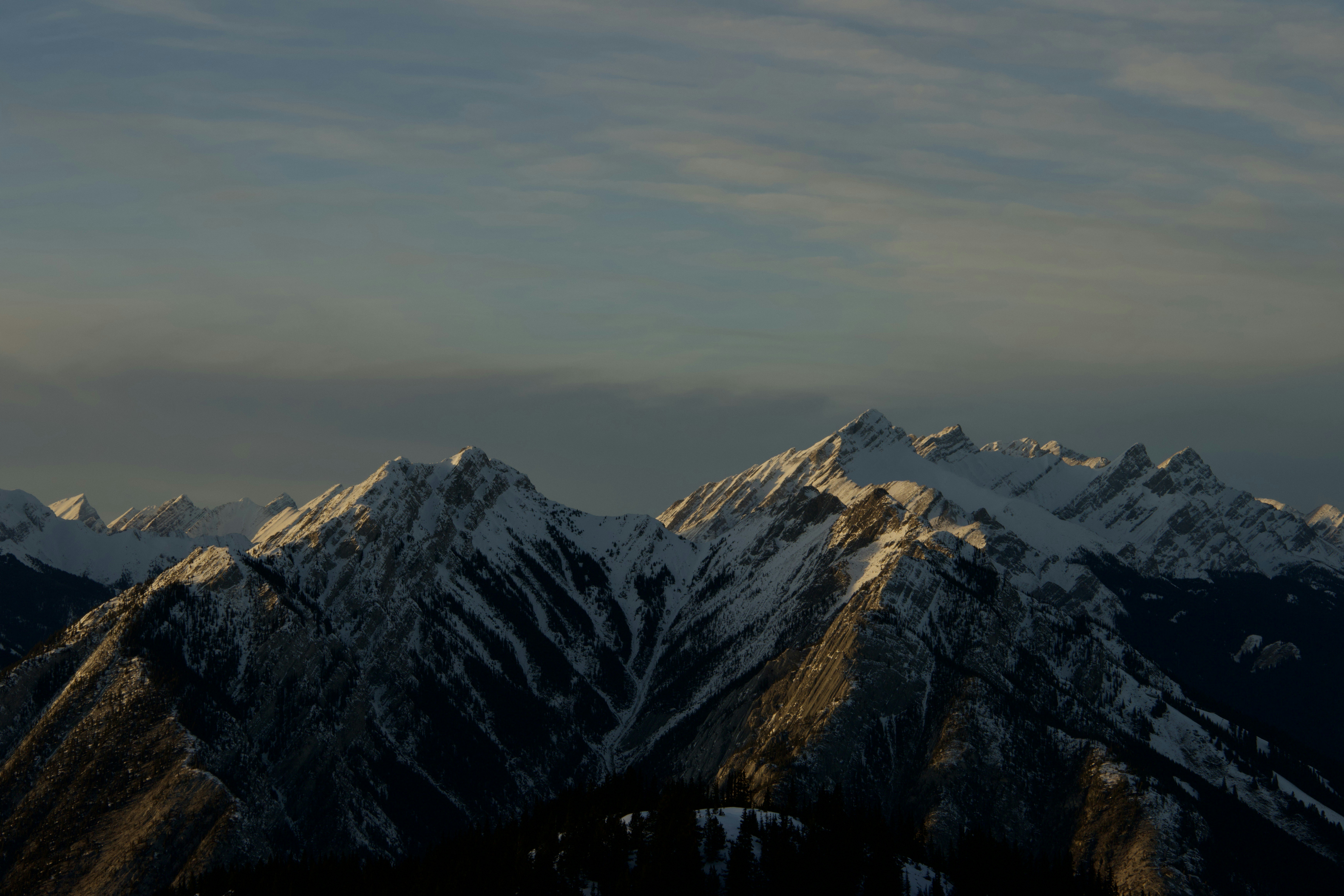 Snow-capped mountains bask in the warm glow of the setting sun beneath a serene sky.