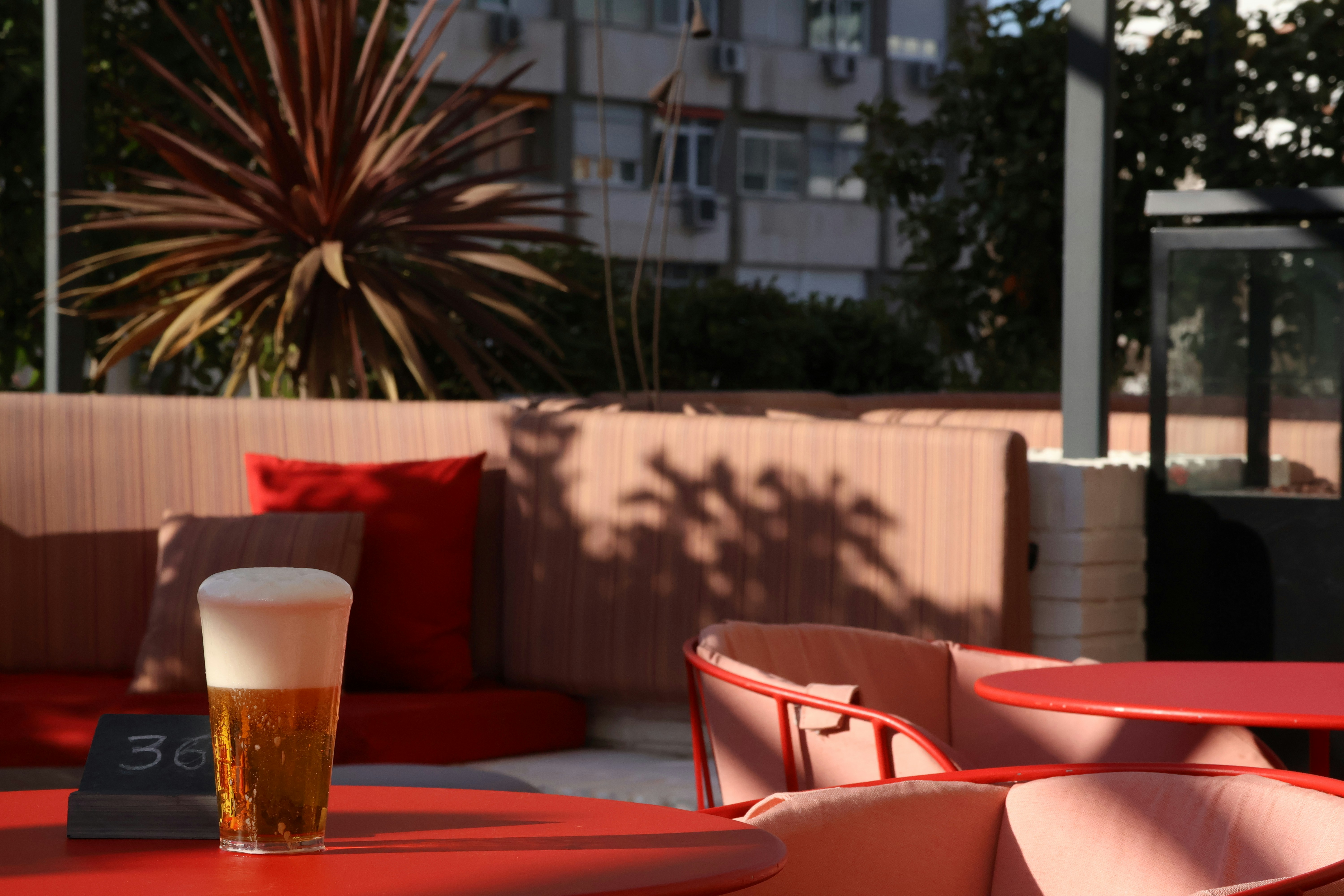 Glass of beer on a red table with sunlight casting shadows on a cozy patio.