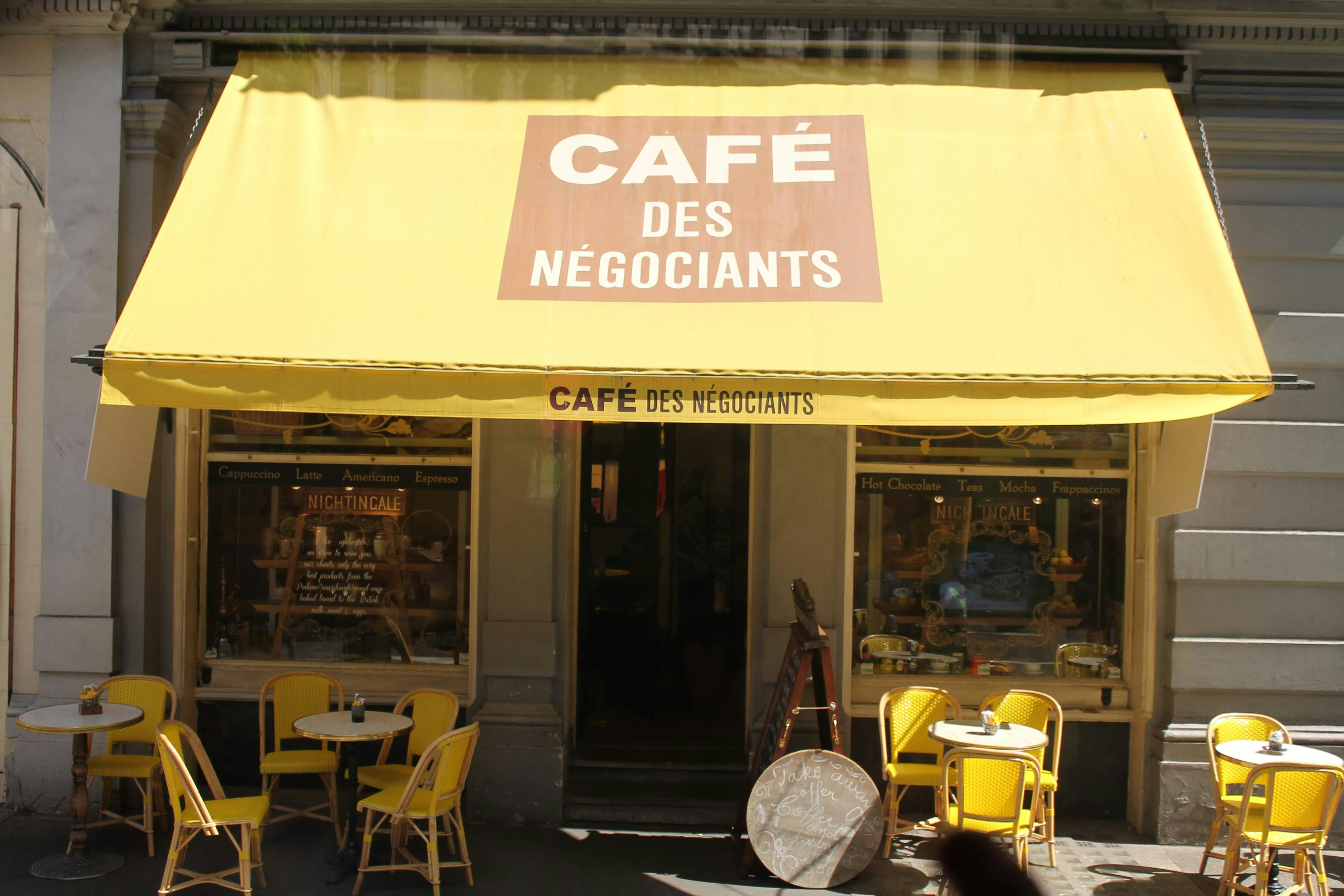 Yellow awning shades outdoor café tables and chairs on a sunny street.