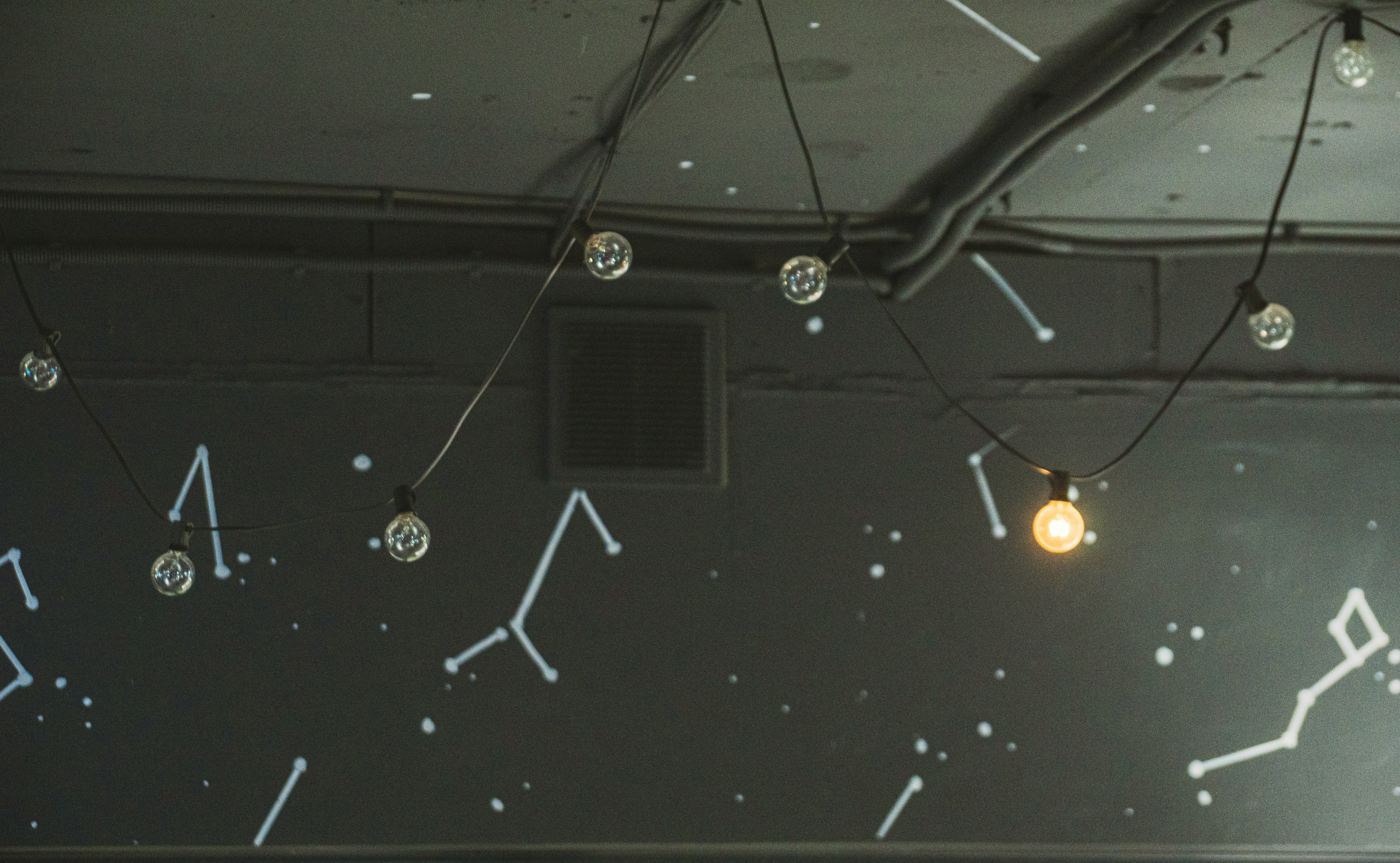 String of light bulbs suspended against a gray ceiling with constellation-patterned wallpaper.