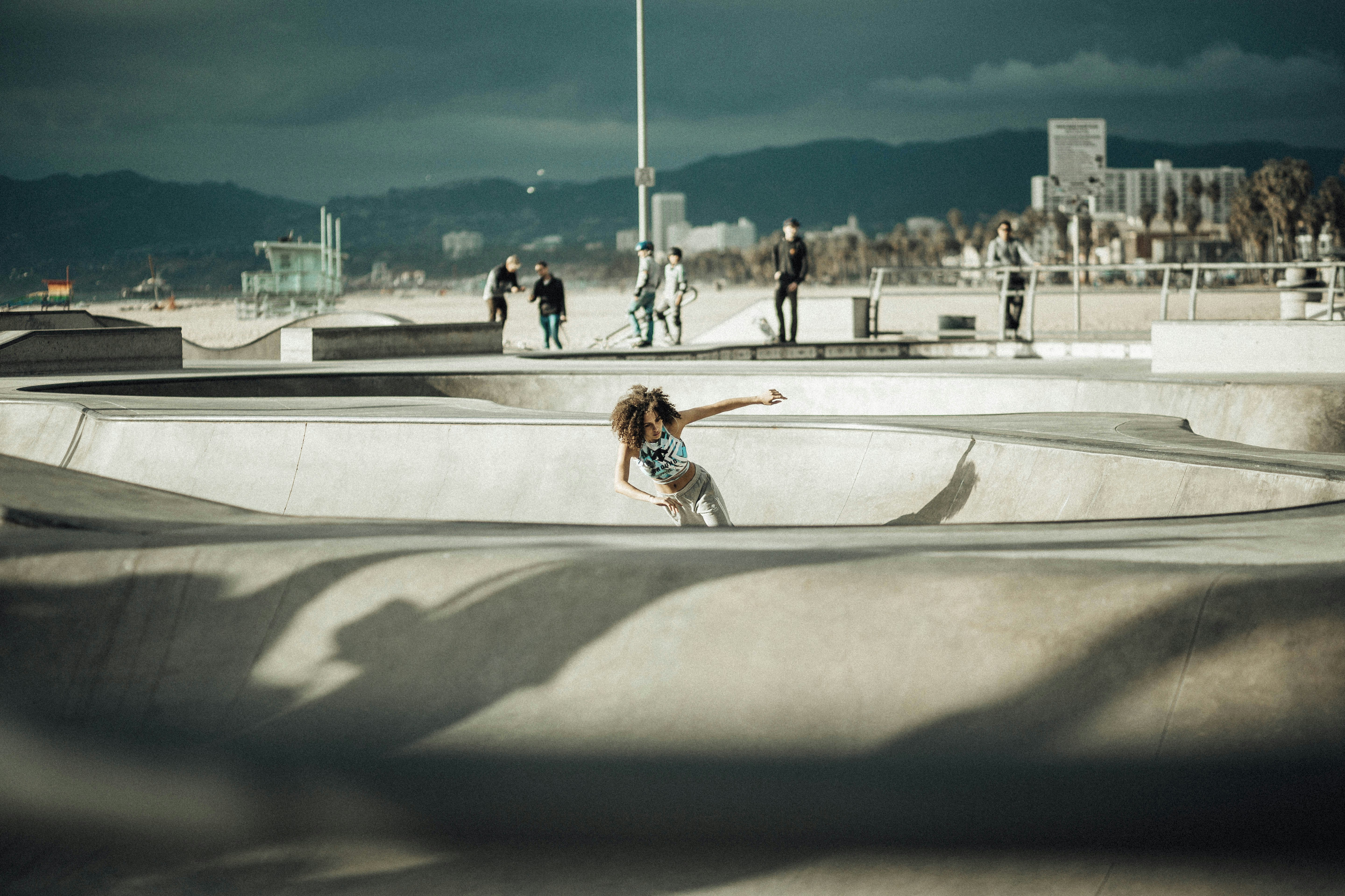 Skateboarder elegantly navigating a smooth concrete skatepark under a moody sky.
