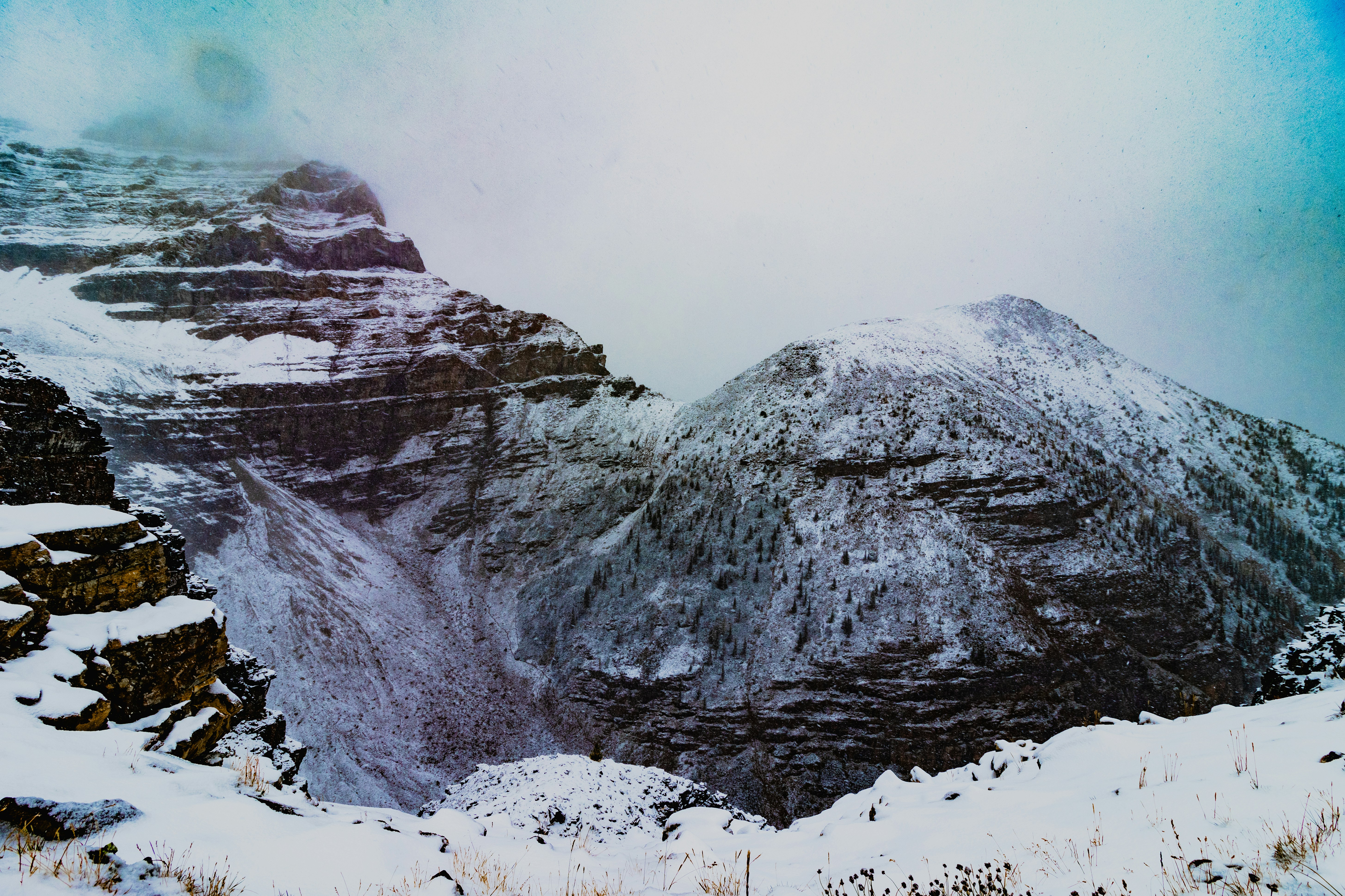 Snow-dusted mountain range under a pale sky, revealing intricate rock formations.