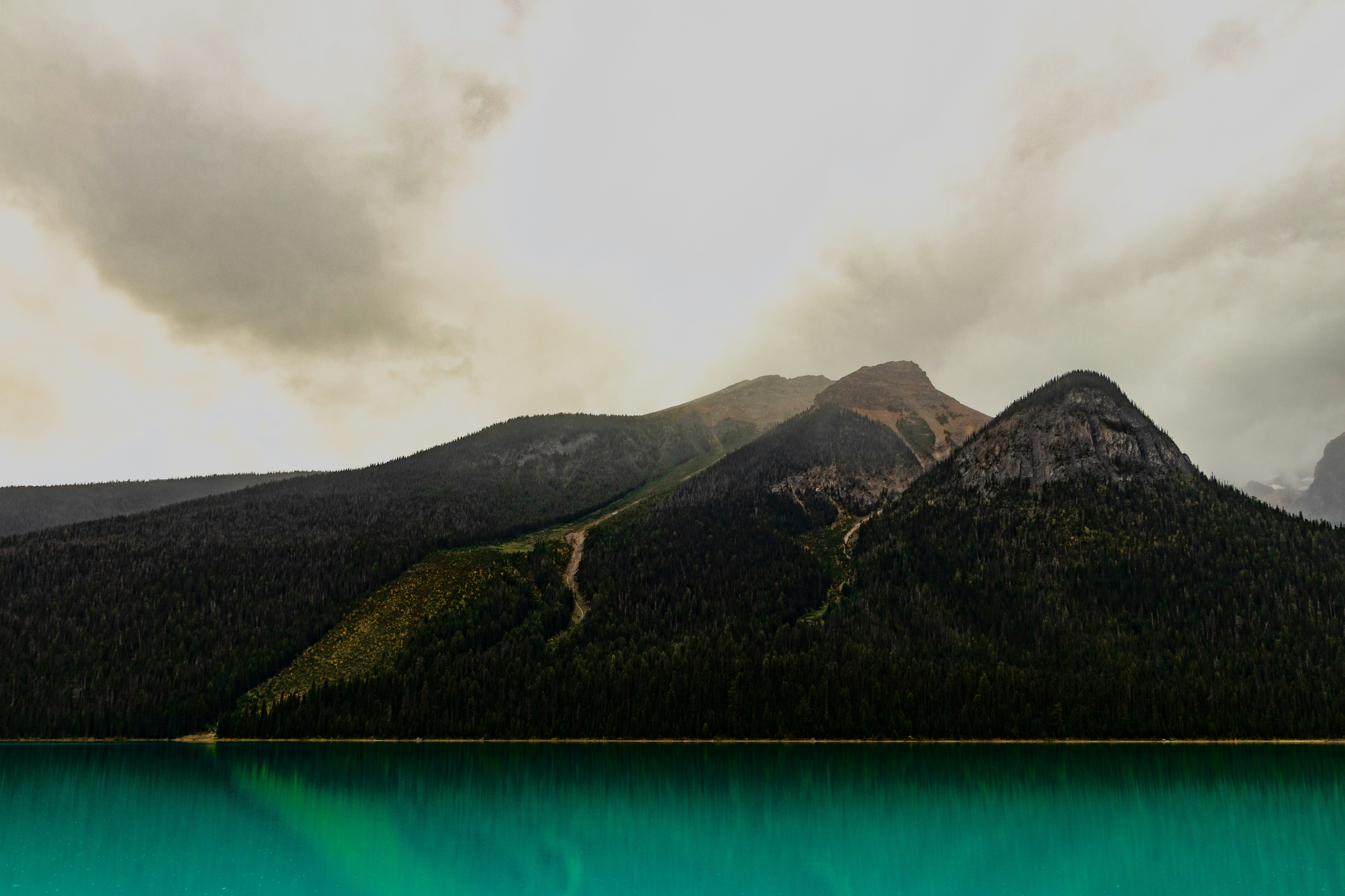 Mountains rise above a vibrant turquoise lake under a cloudy sky.
