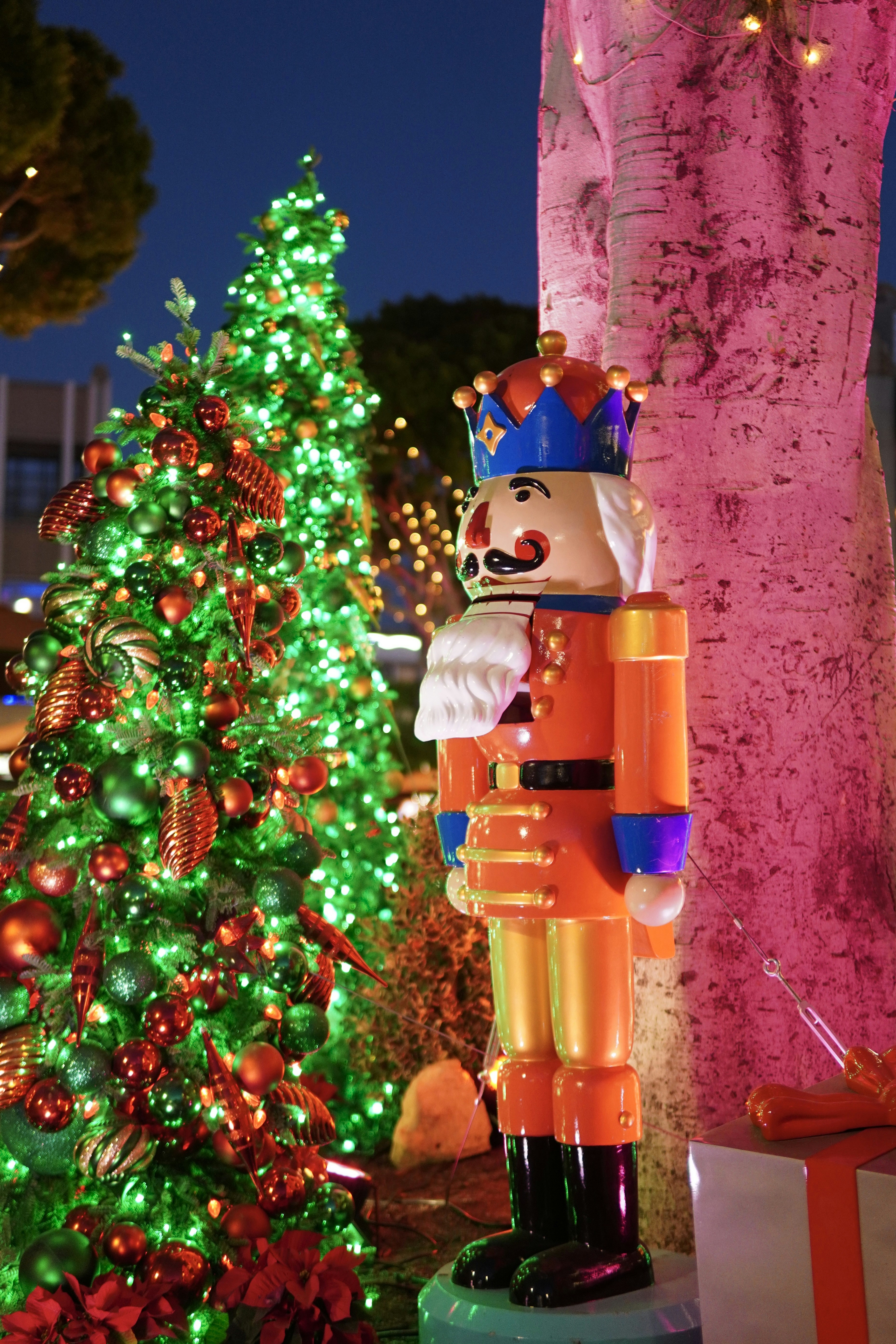 A colorful nutcracker statue stands proudly beside a vibrant Christmas tree adorned with sparkling lights and ornaments, creating a festive atmosphere.