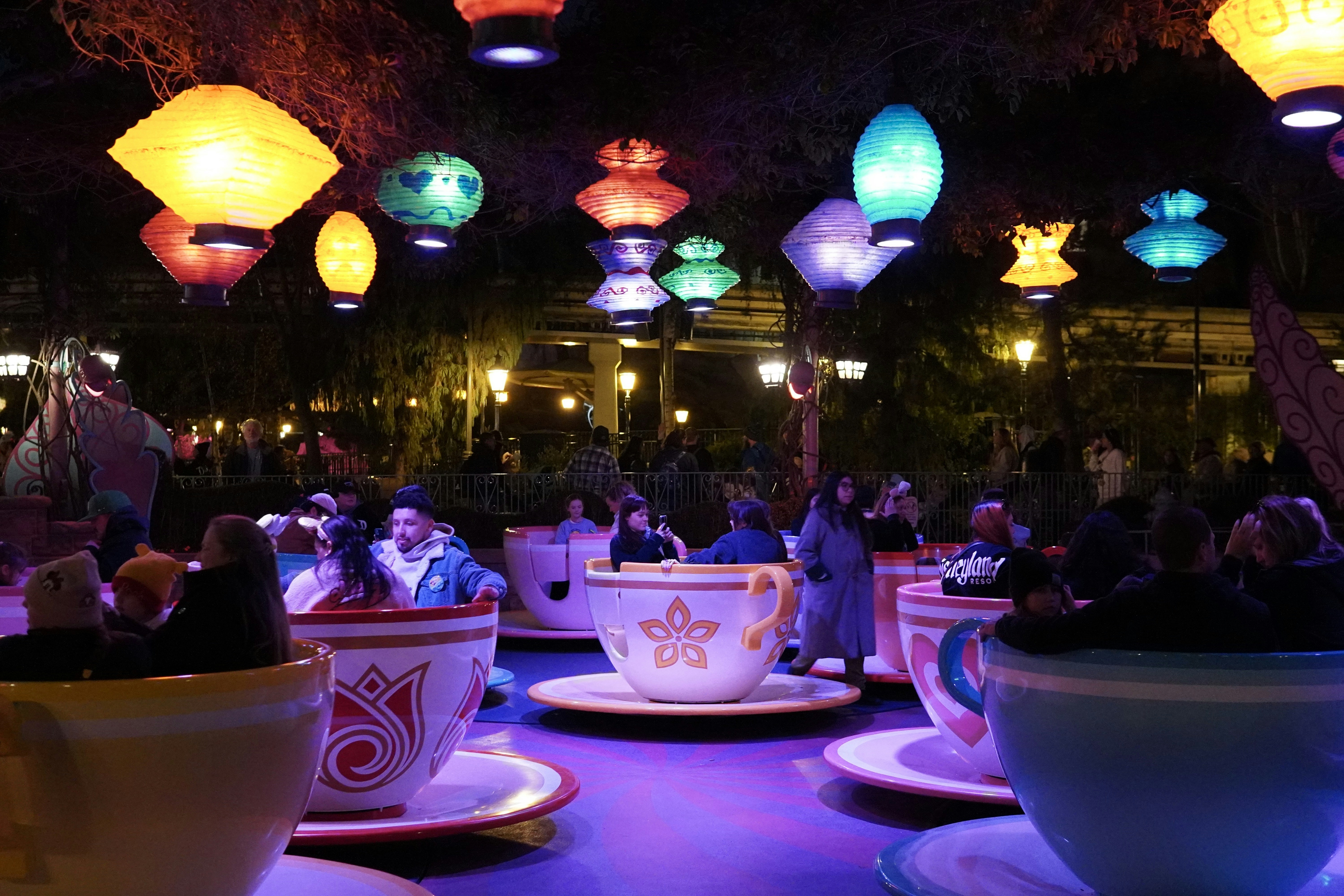 Colorful teacups spin under vibrant lanterns at night, creating a whimsical atmosphere filled with laughter.
