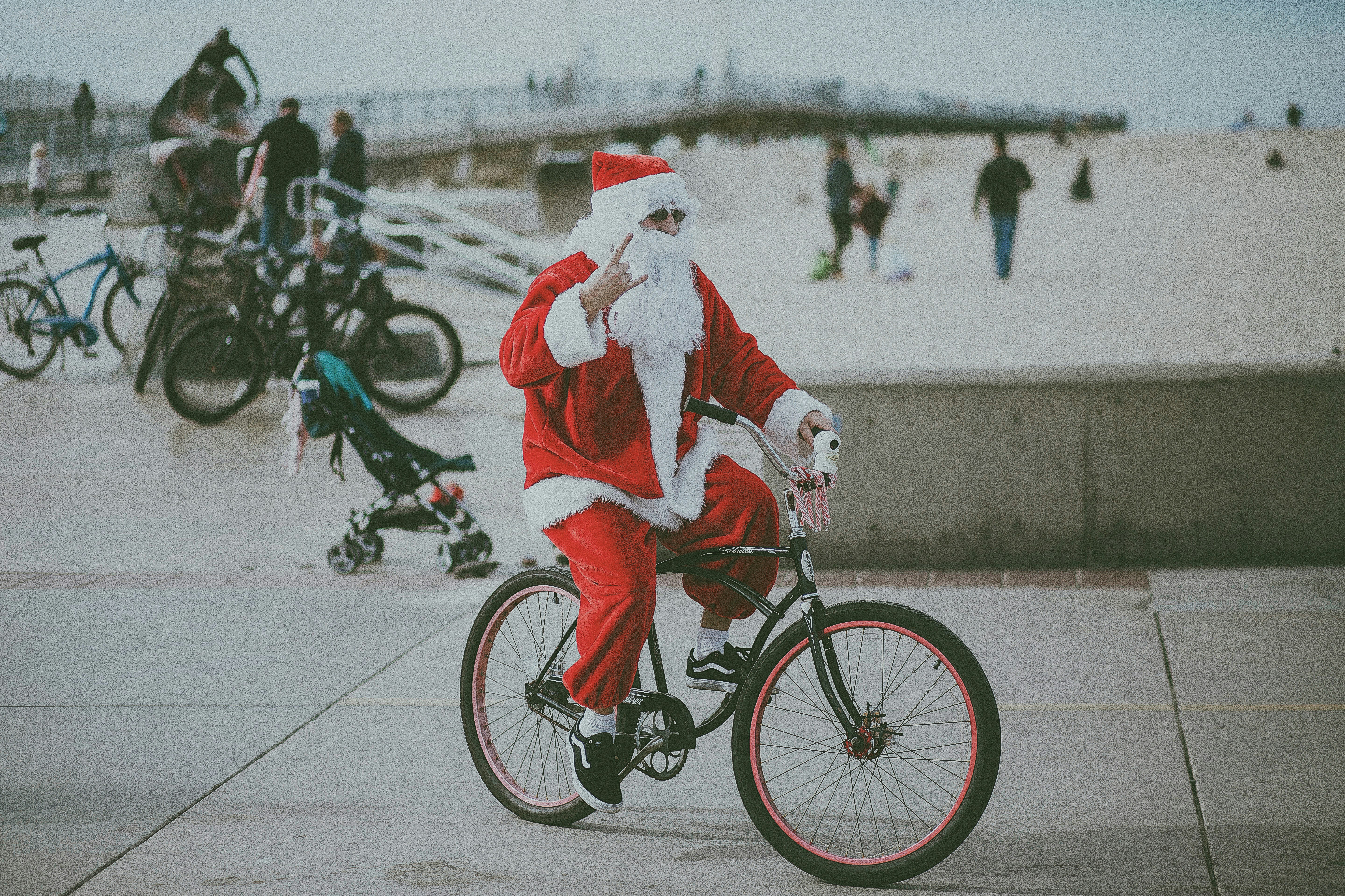 Santa Claus riding a bicycle along a beachfront promenade.