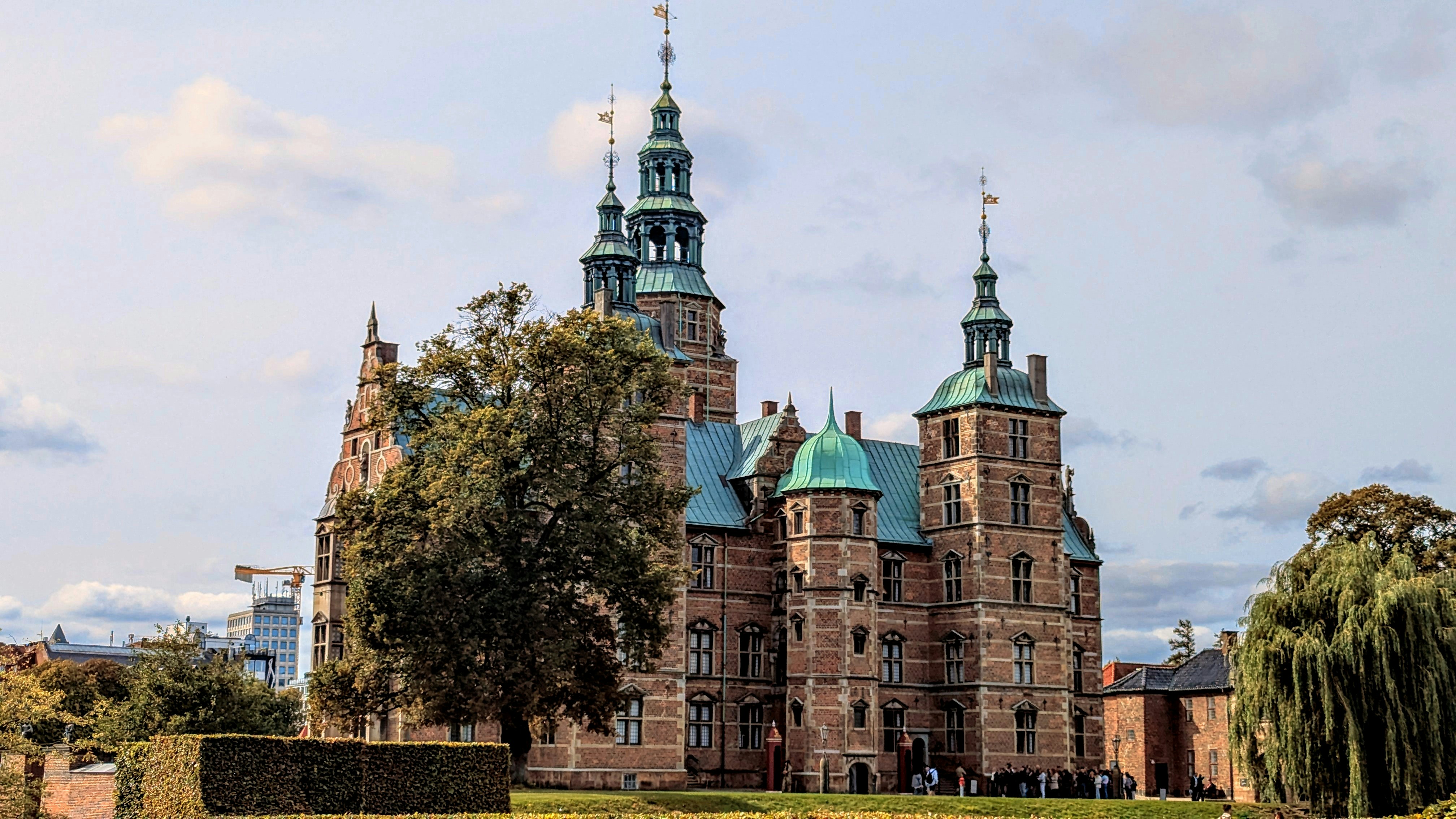 Historic castle with intricate towers and verdant surroundings under a cloudy sky.