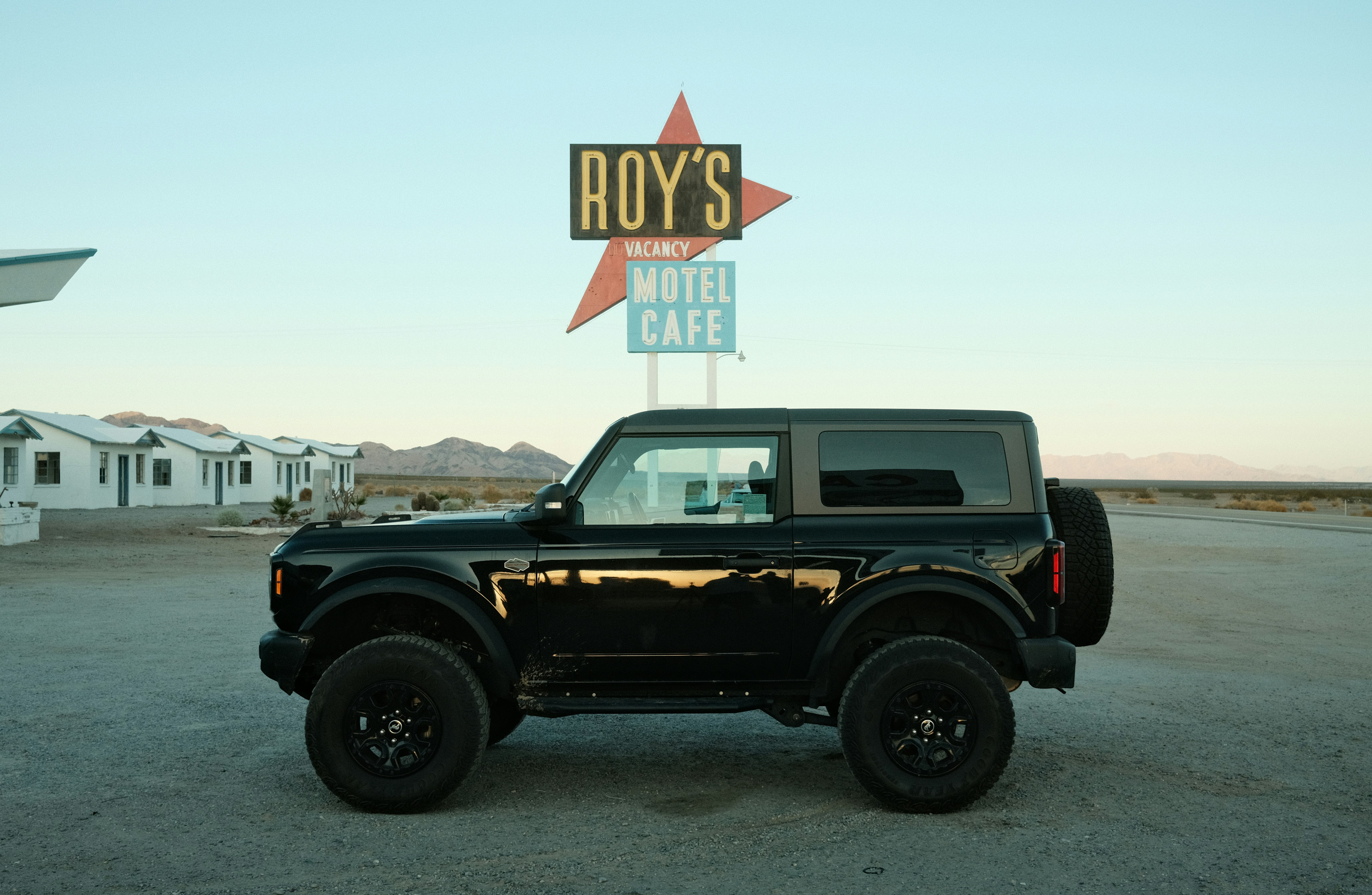 Black SUV parked in front of Roy's Motel sign with desert landscape at sunrise.