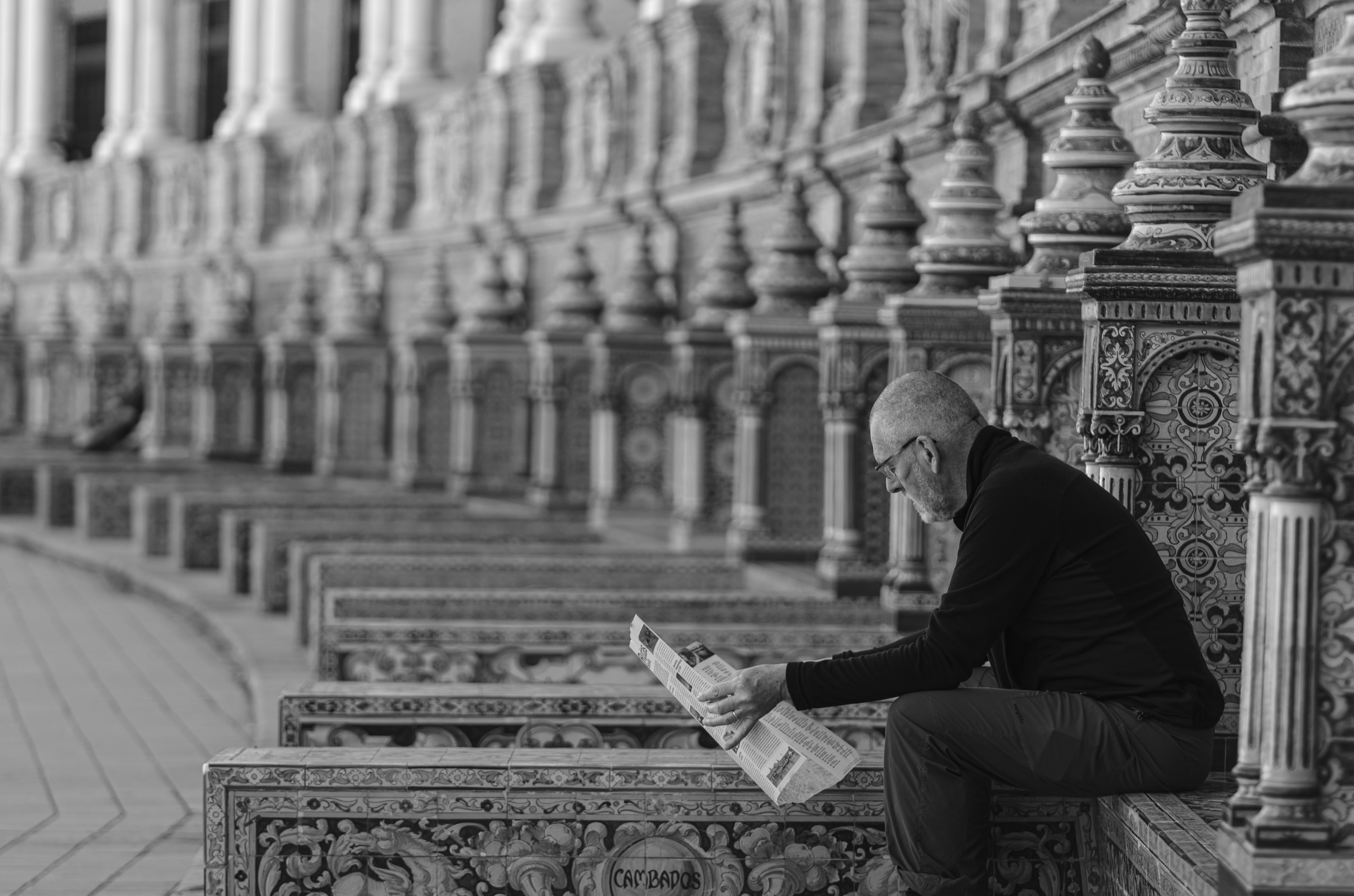 Person seated on a decorated bench reading a newspaper by a line of elaborate columns.